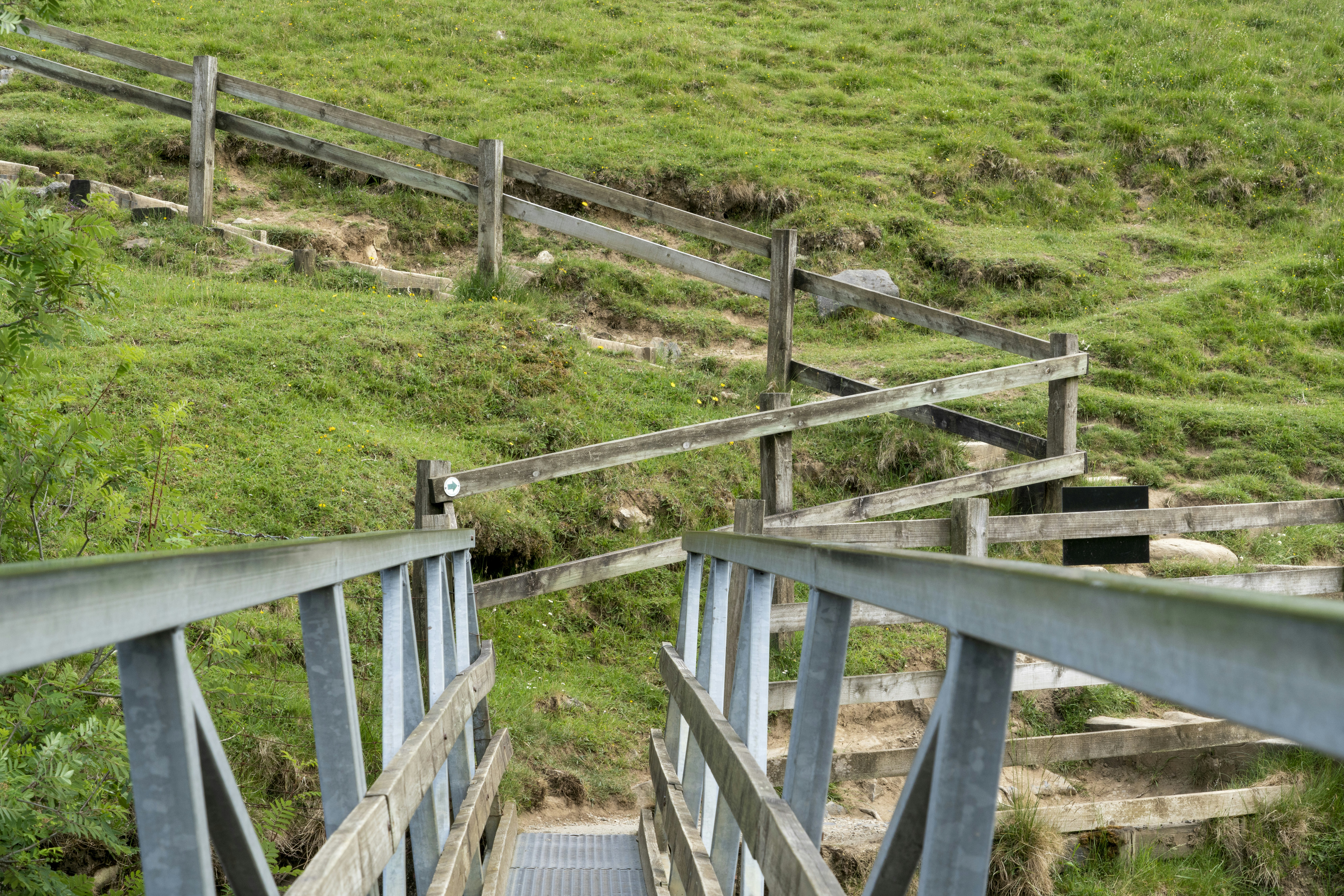Wooden bridge leading down to a lush green pasture with rustic fencing in the background.