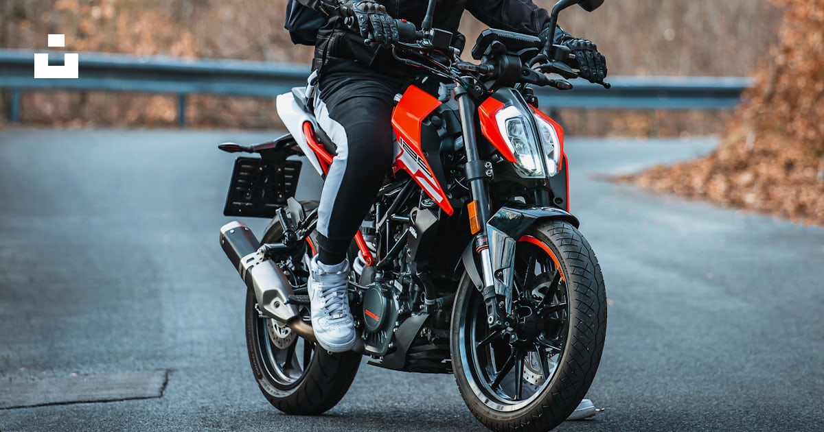 昼間の道路でオレンジと黒のバイクに乗る黒いジャケットの男の写真 Unsplashのオートバイの無料画像