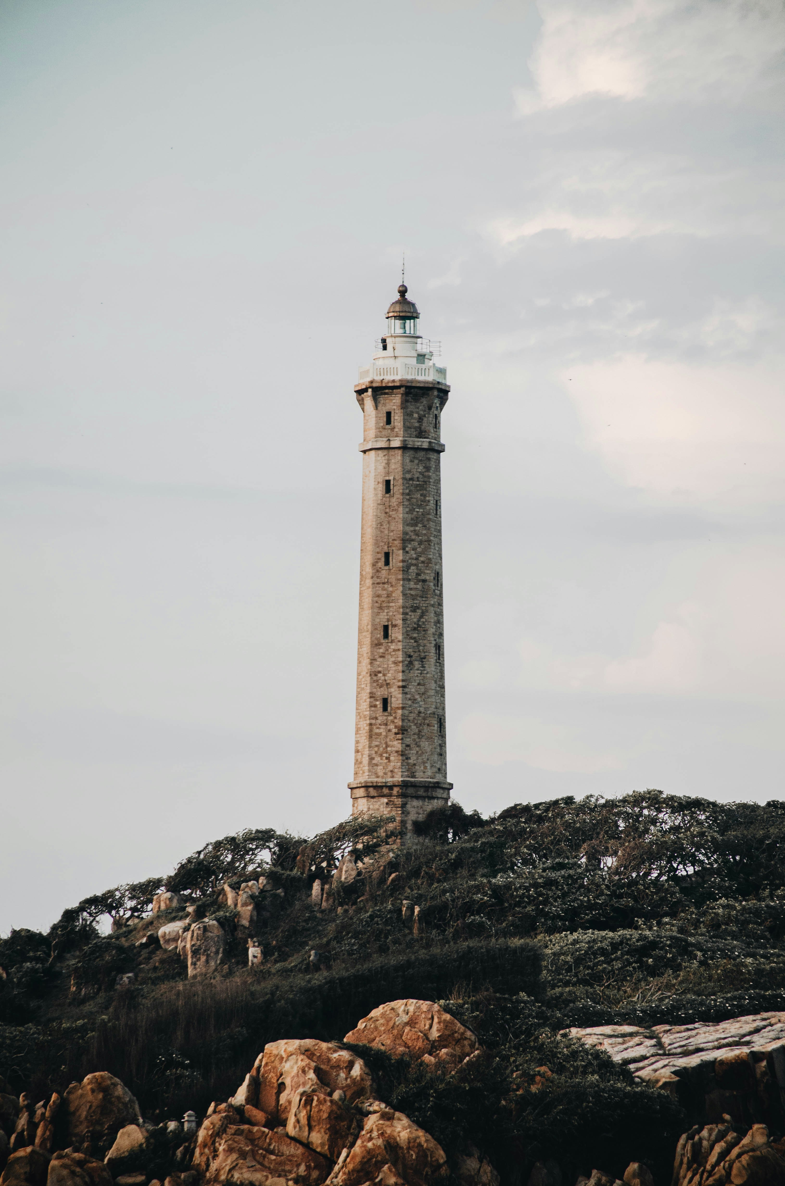 A majestic lighthouse standing tall on a rocky coastline, surrounded by lush greenery and rugged terrain.