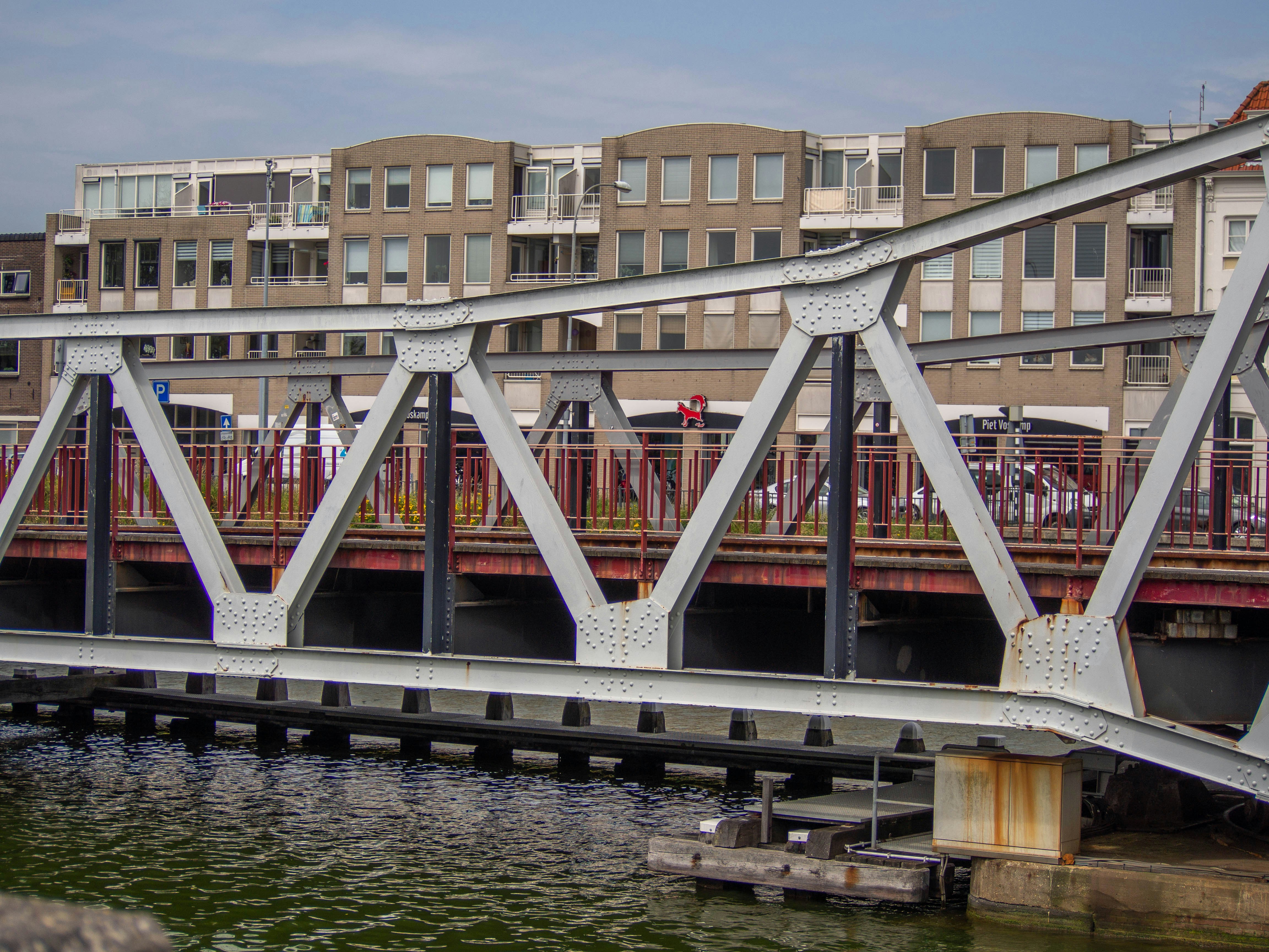Steel bridge spanning a calm waterway, with contemporary buildings in the background. The scene reflects urban architecture and infrastructure.