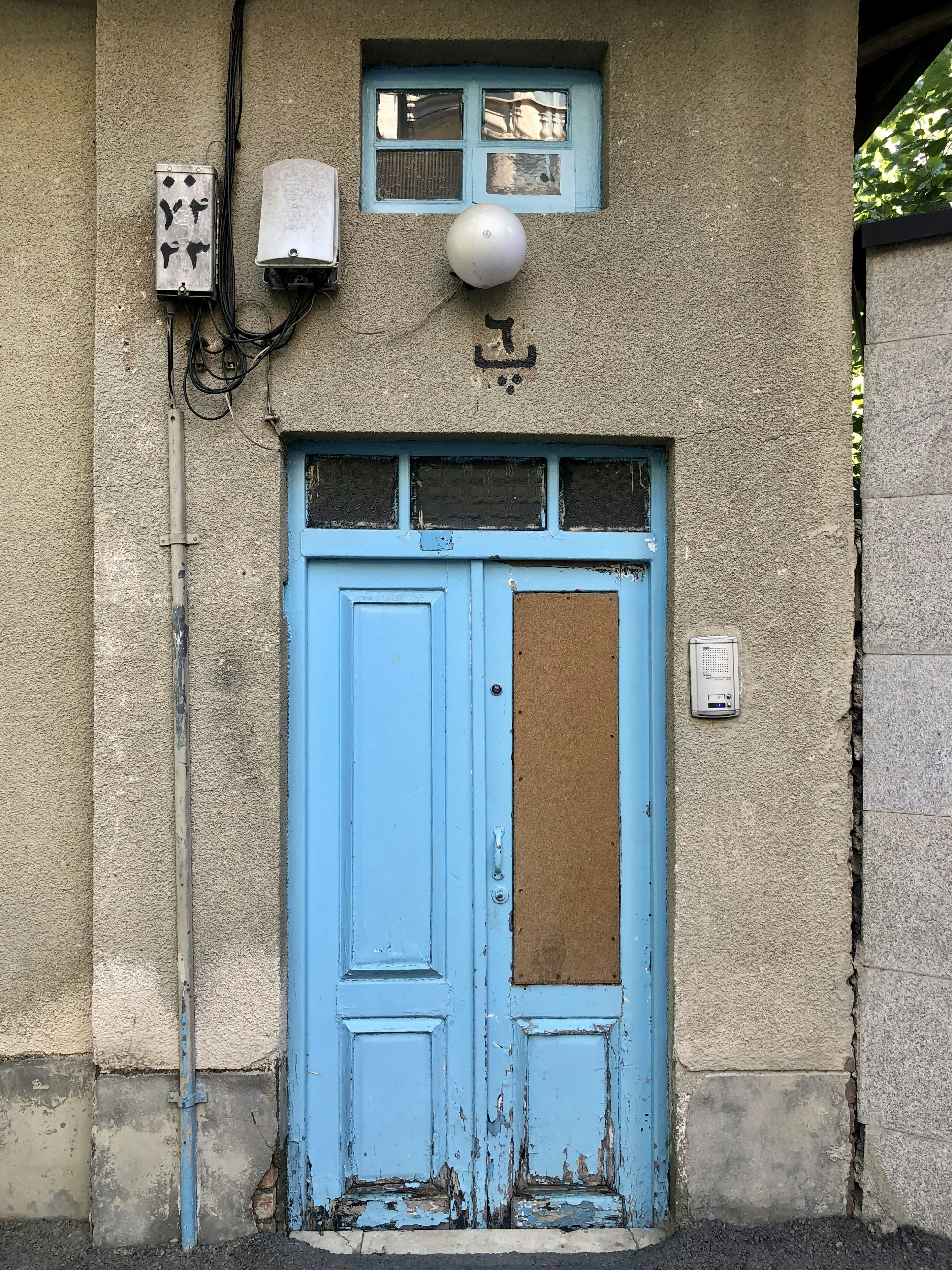 Azure Doorway: Weathered Panels Beneath a Small Window on a Textured Facade