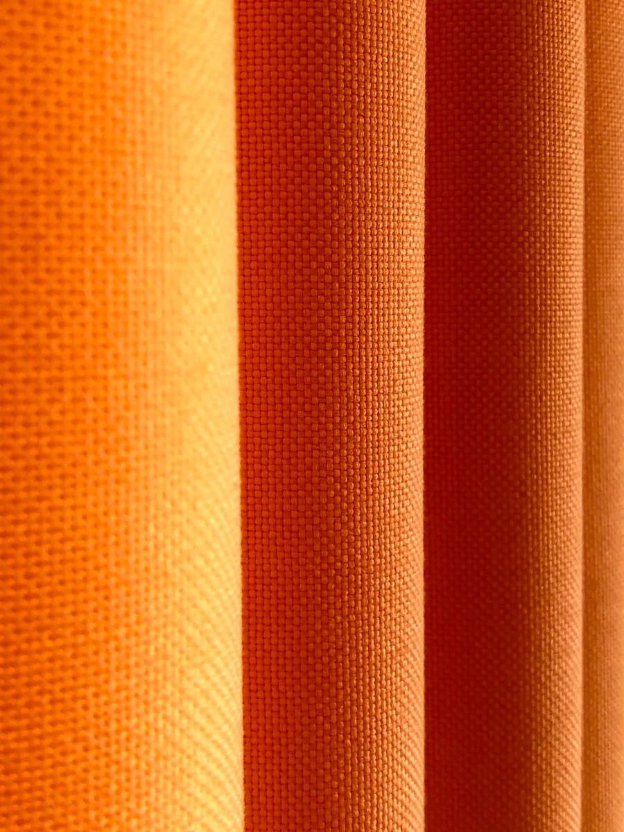 Close-up of orange and amber woven fabric with vertical folds and textured weave. The soft light creates rich gradients across the material.