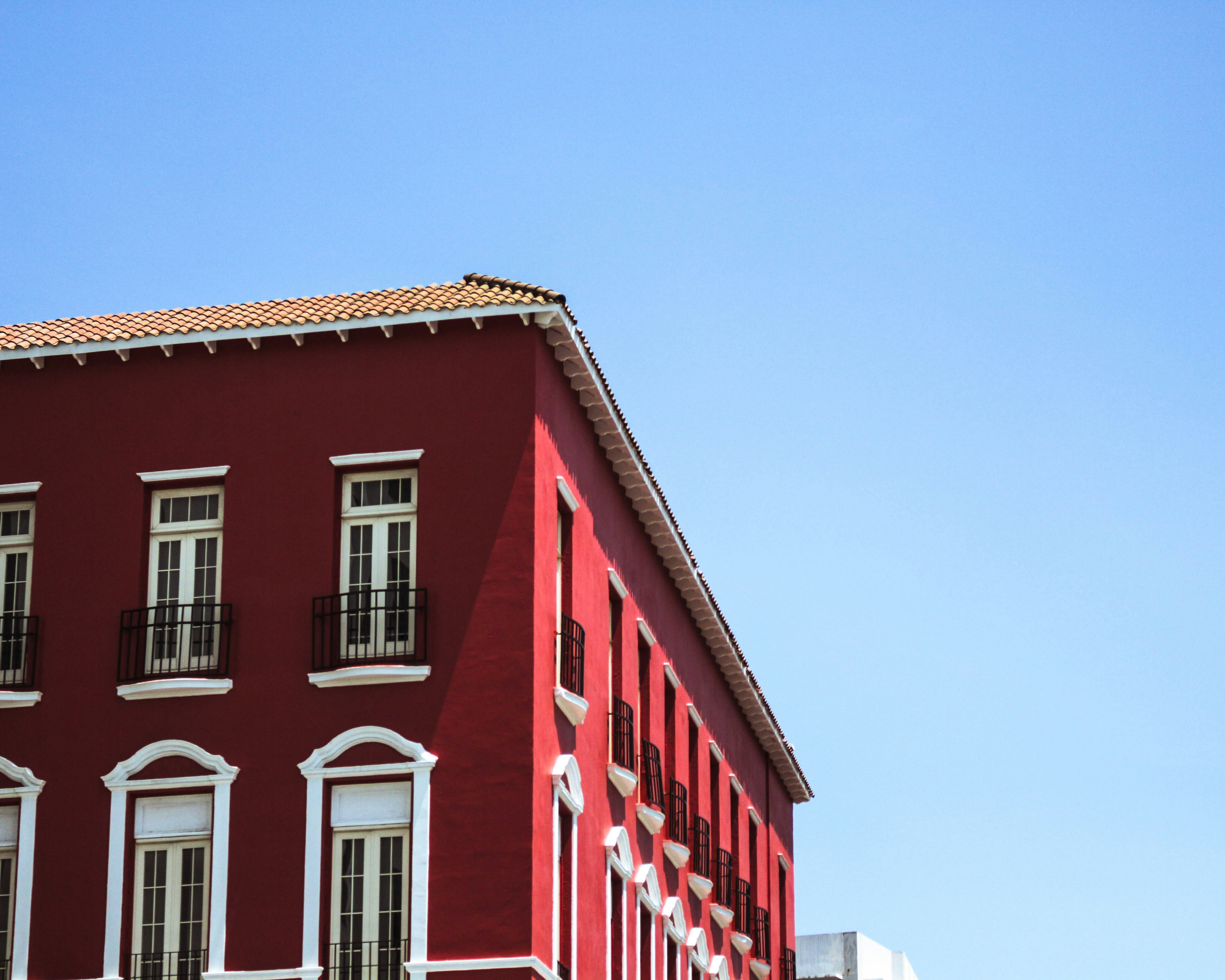Red and white building corner with classic windows set against a clear blue sky.
