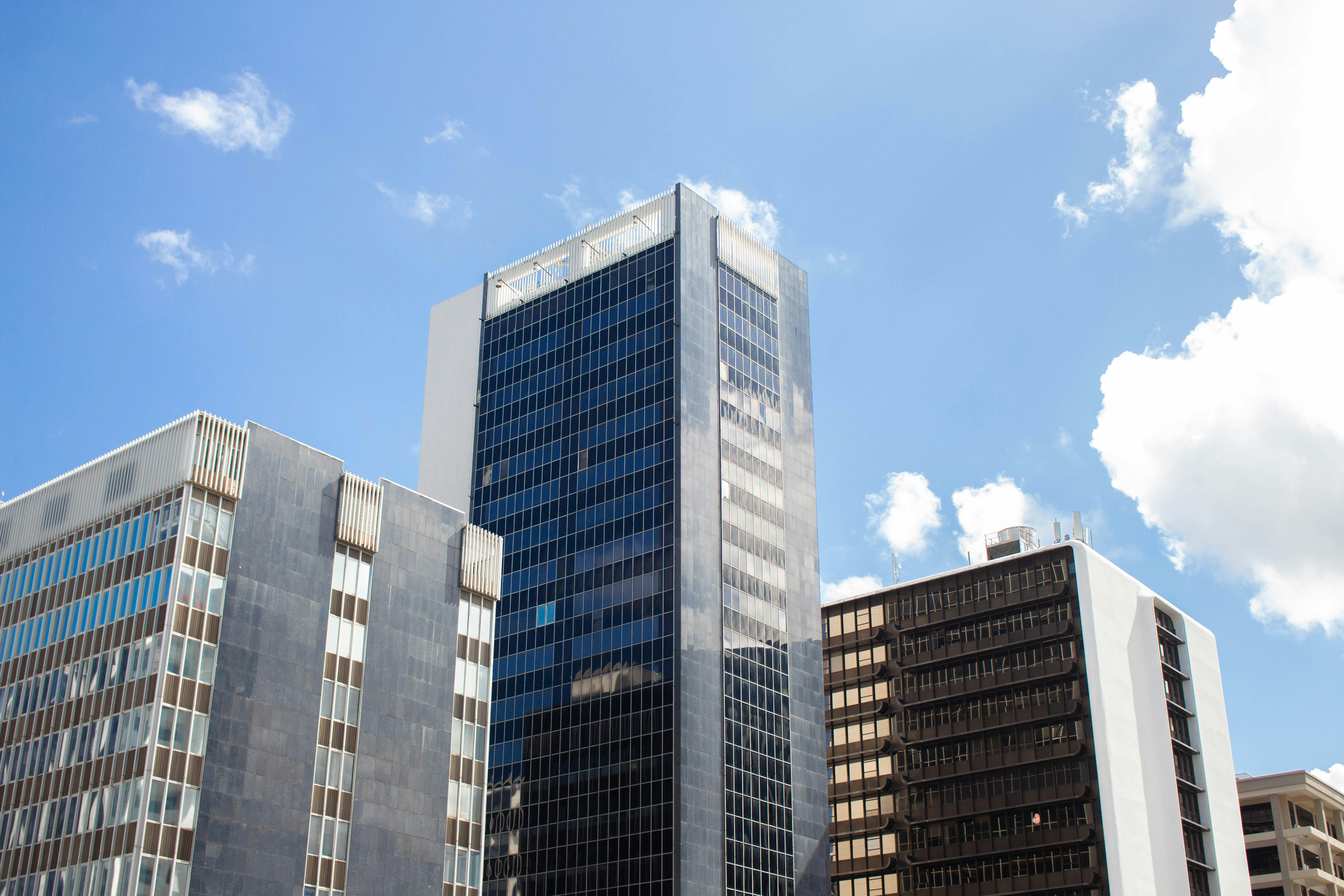 Tall modern buildings rise against a bright blue sky with scattered clouds.