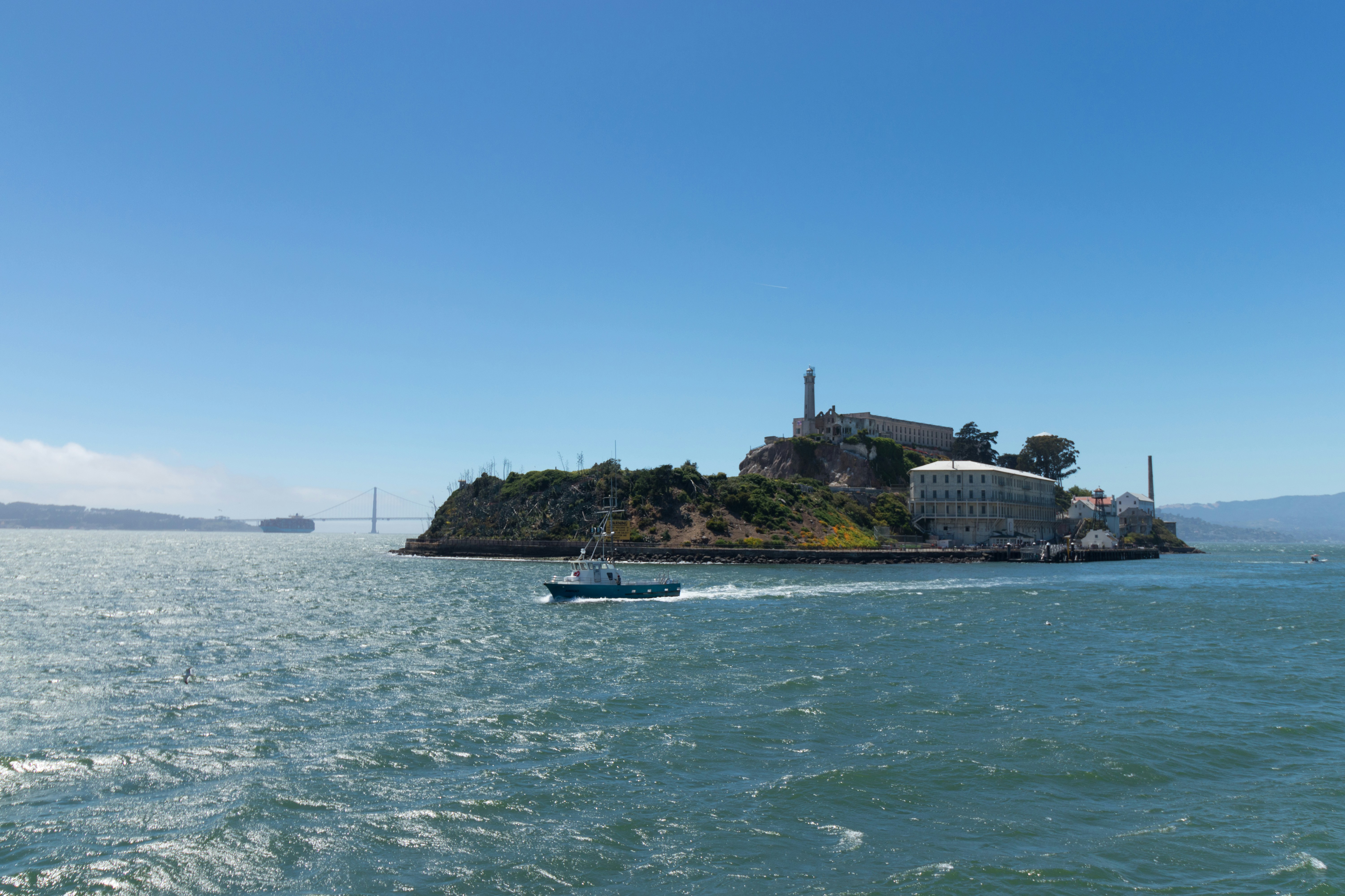 Alcatraz Island with its historic buildings and a boat navigating the waters, under a clear blue sky. The scene captures the essence of this iconic landmark.