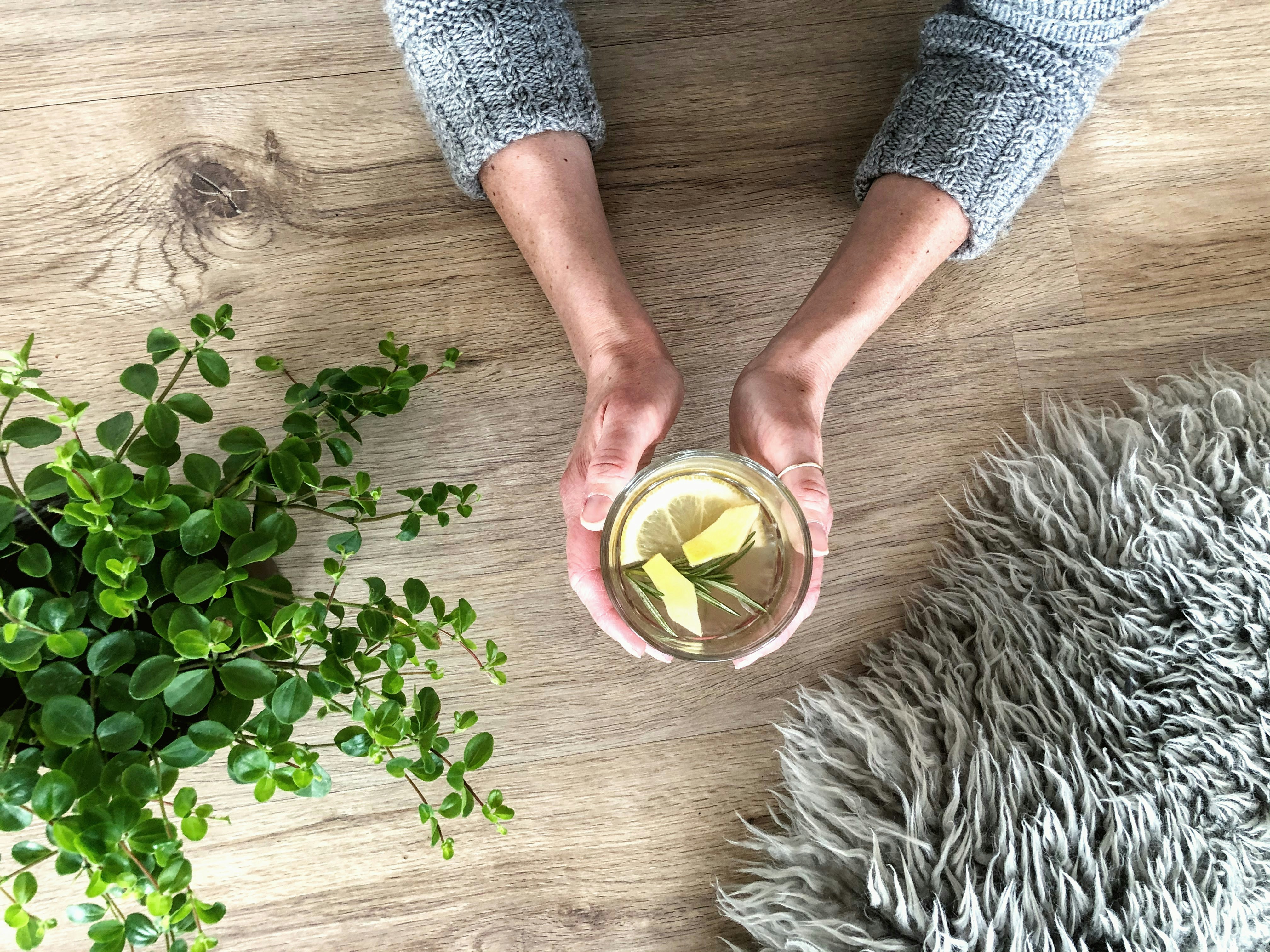 Hands around a glass of lemon water on a wooden table