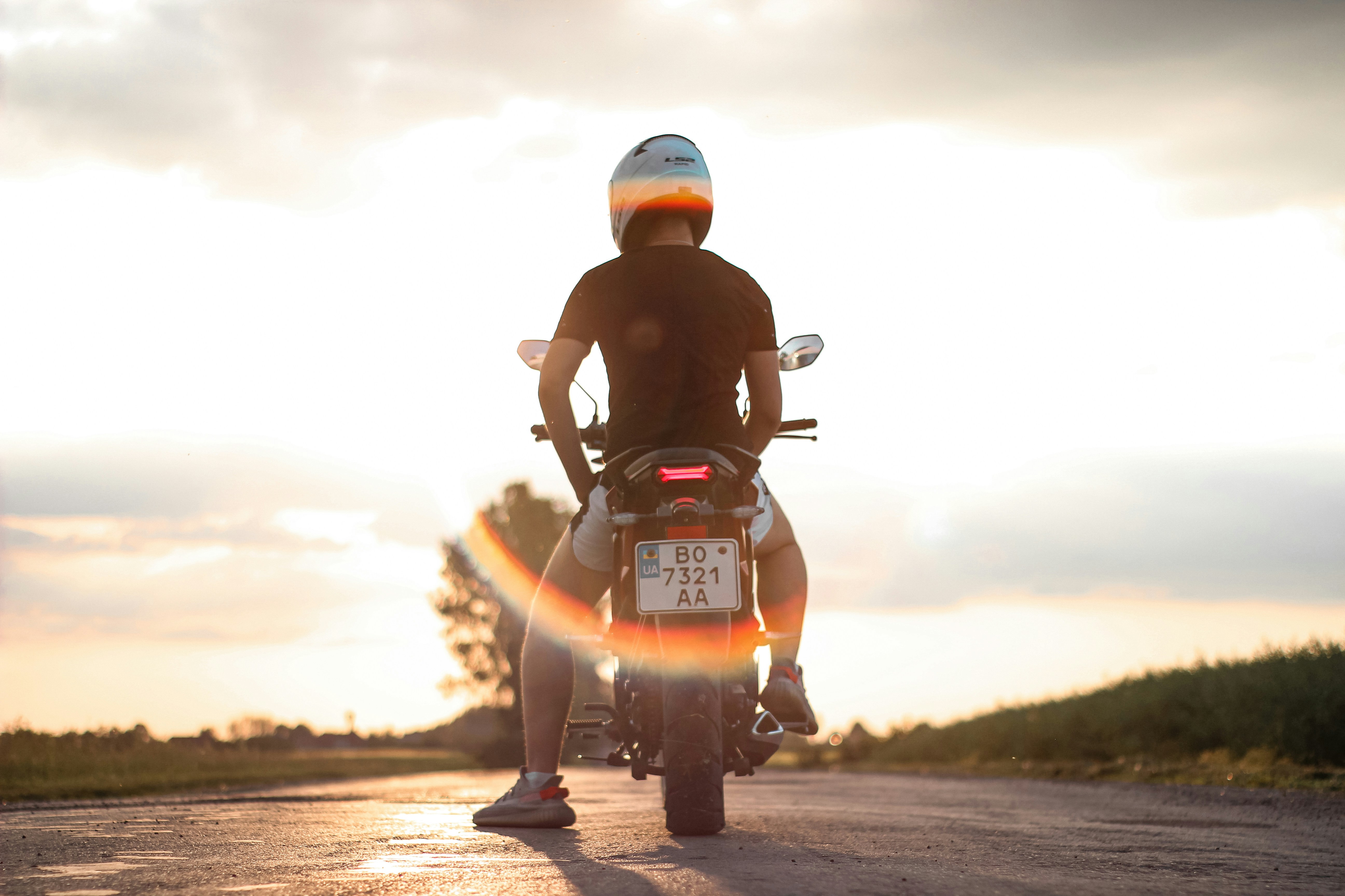 Motorcyclist sitting on a bike, facing a sunset-lit road, creating a sense of adventure and introspection.