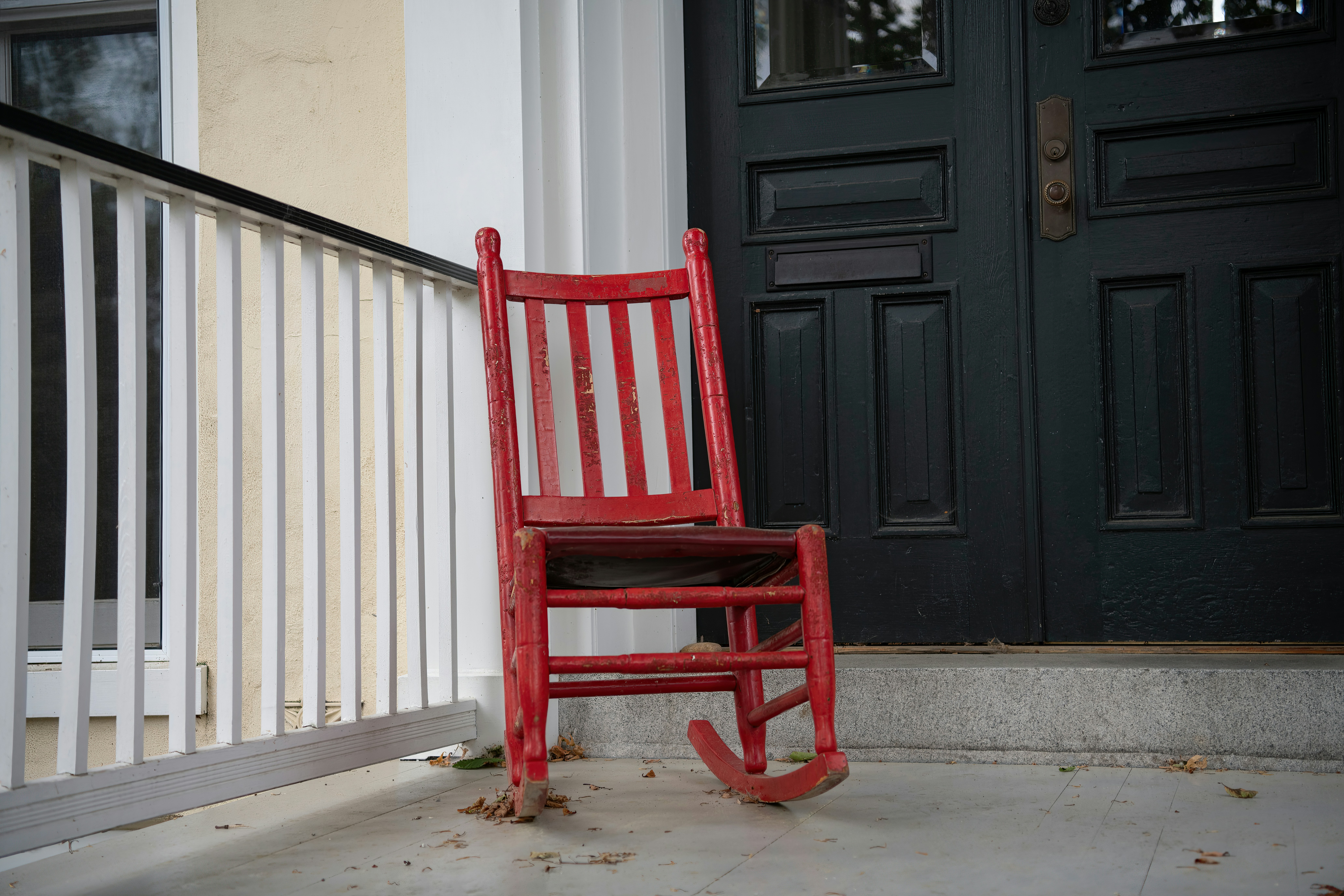 A weathered red rocking chair sits invitingly on a porch, framed by a backdrop of classic black doors and white railings.