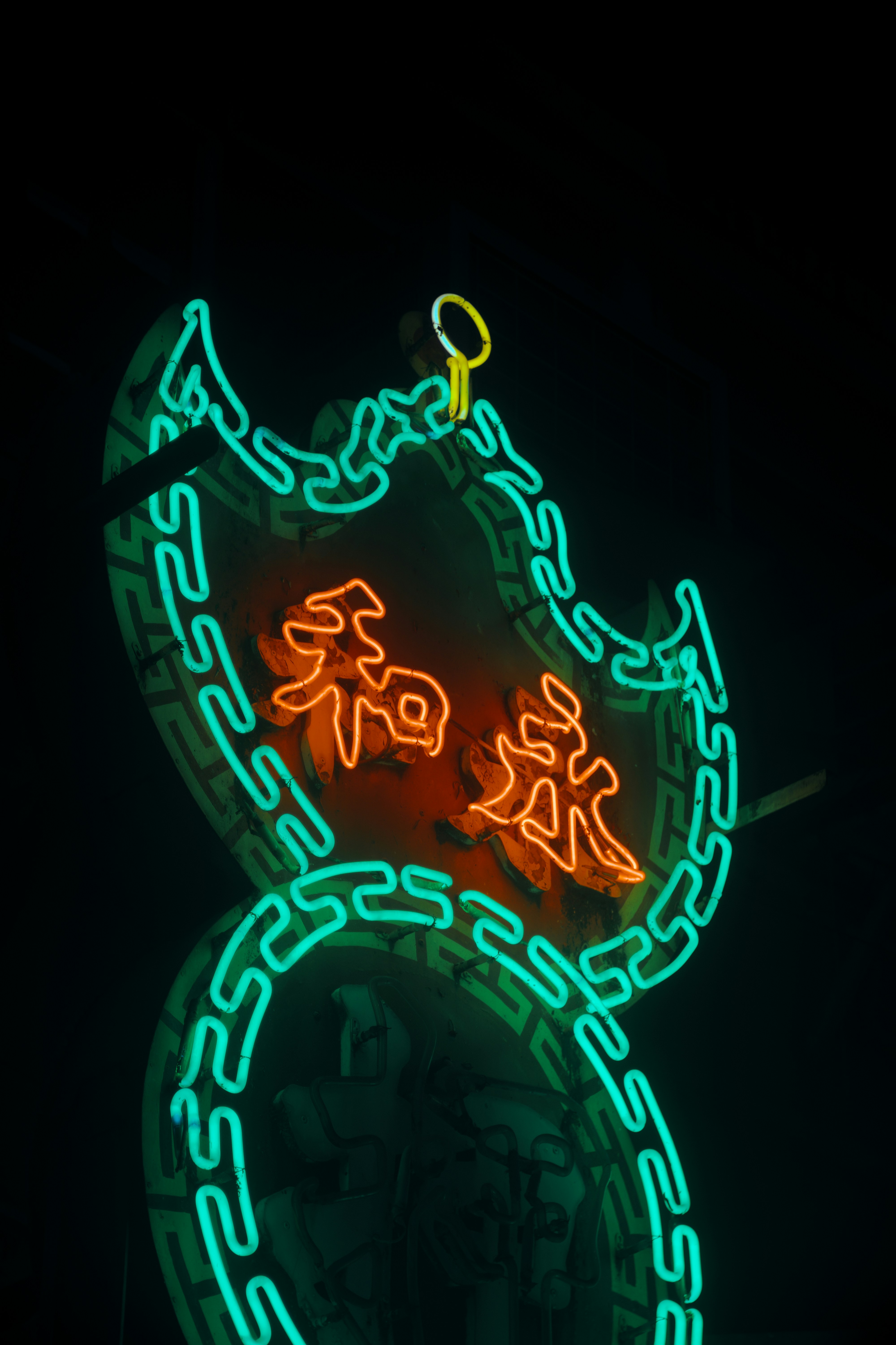 Vibrant neon sign featuring intertwined chains and Chinese characters, radiating a warm glow against a dark backdrop.