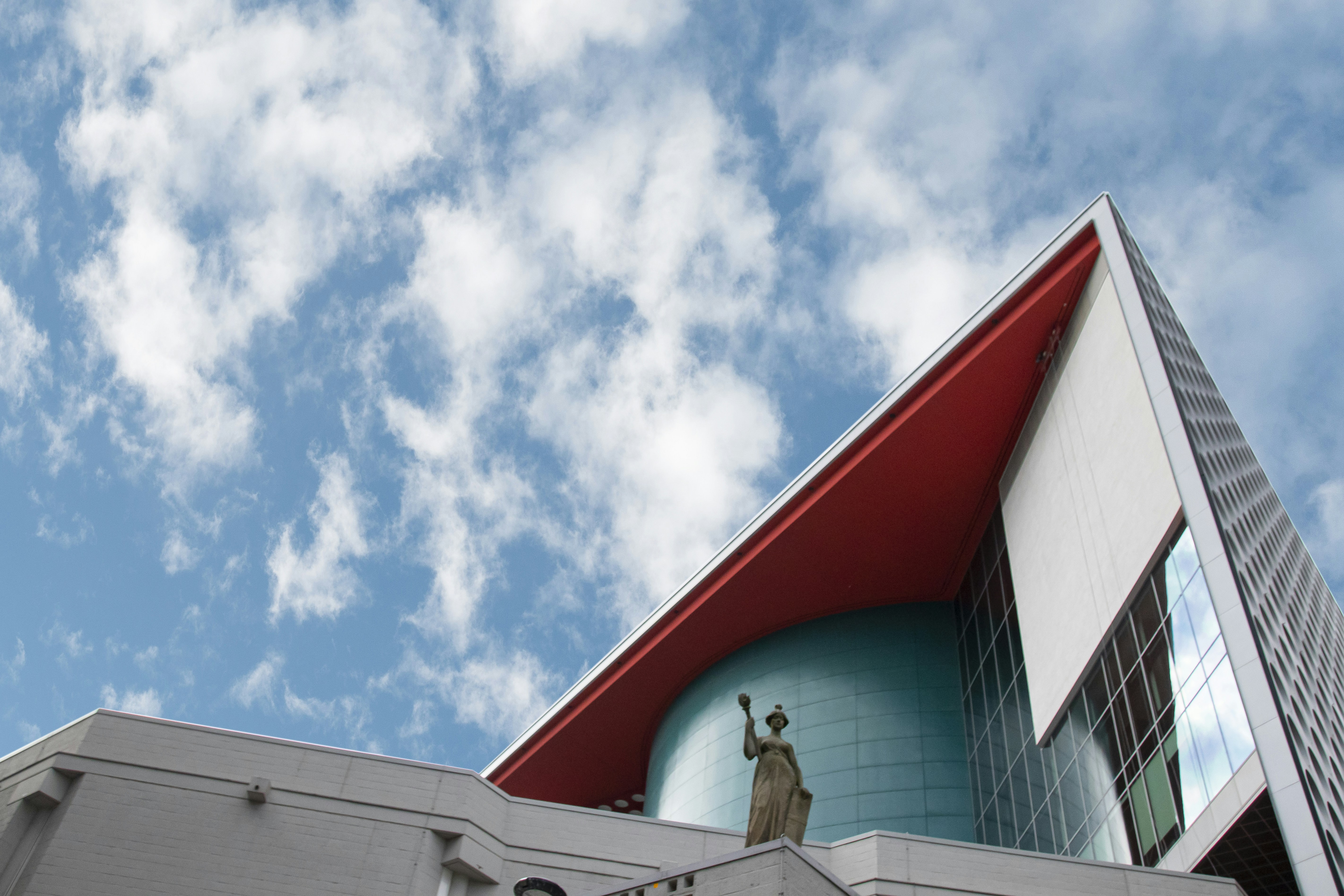 Modern architectural structure with bold red accents and a statue under a partly cloudy sky.