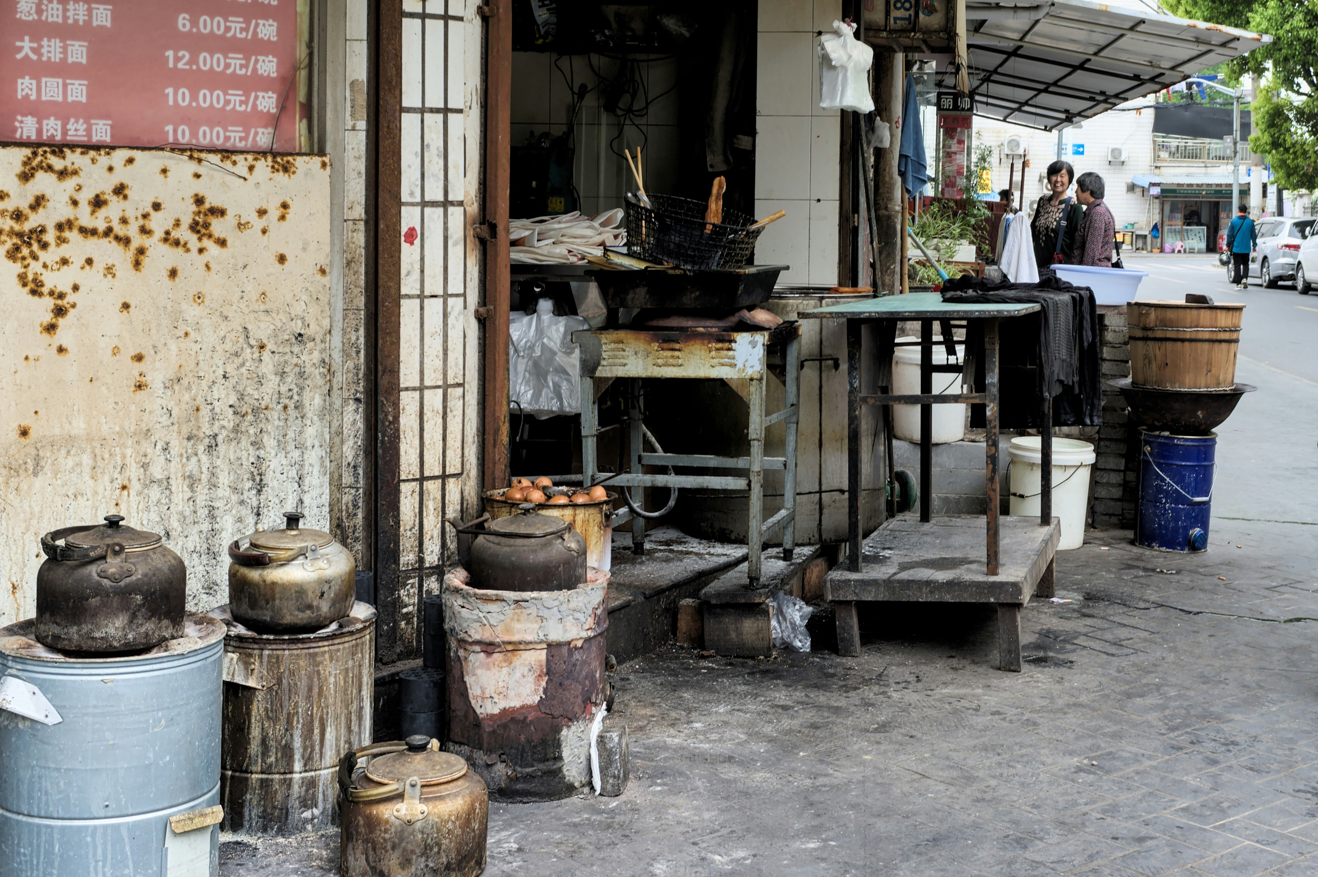 Weathered cooking pots and utensils line a bustling street vendor's stall, showcasing the essence of local cuisine. A faded menu hints at the culinary offerings available.