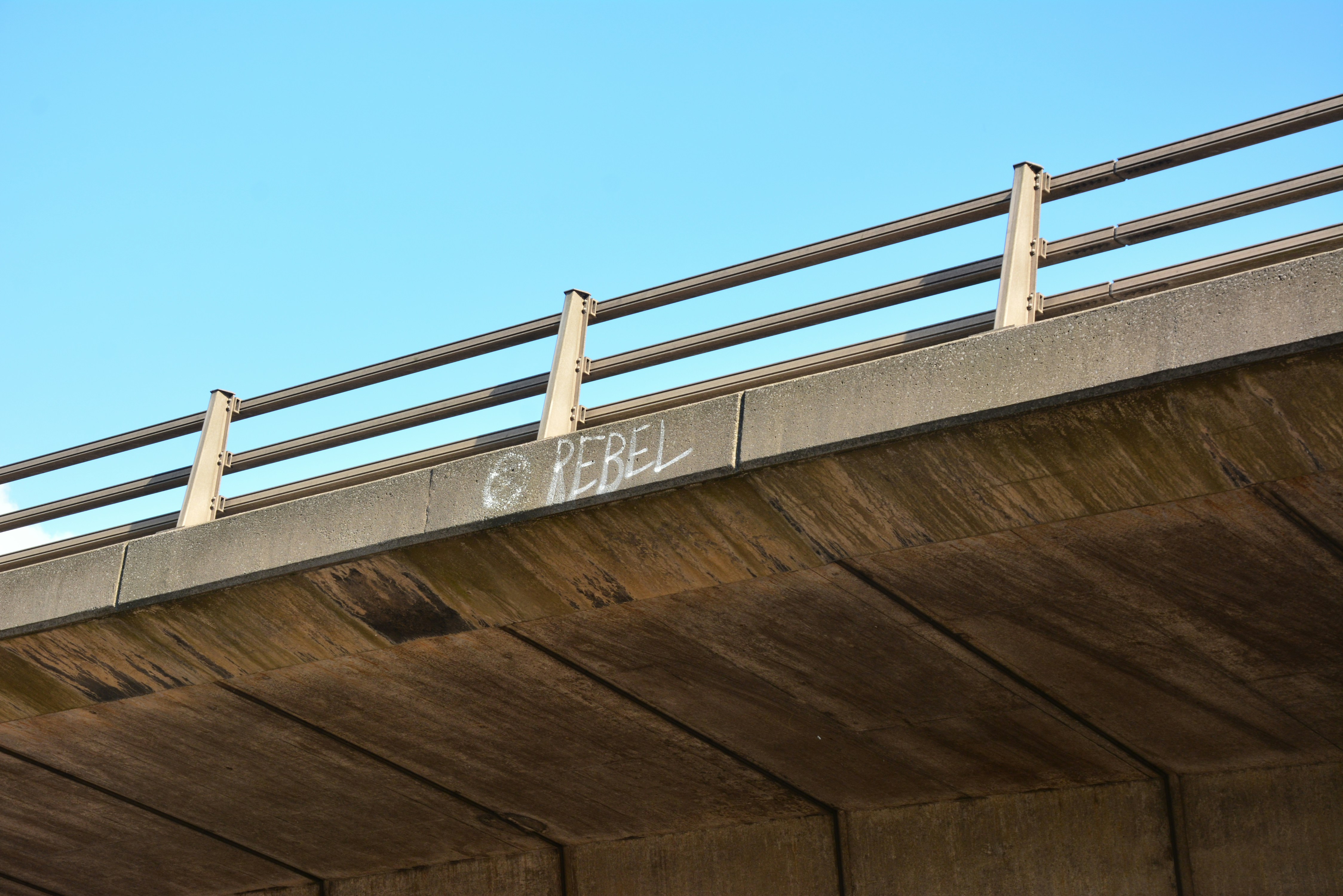 Graffiti reading 'REBEL' on a concrete overpass, showcasing urban art's defiance against the mundane.