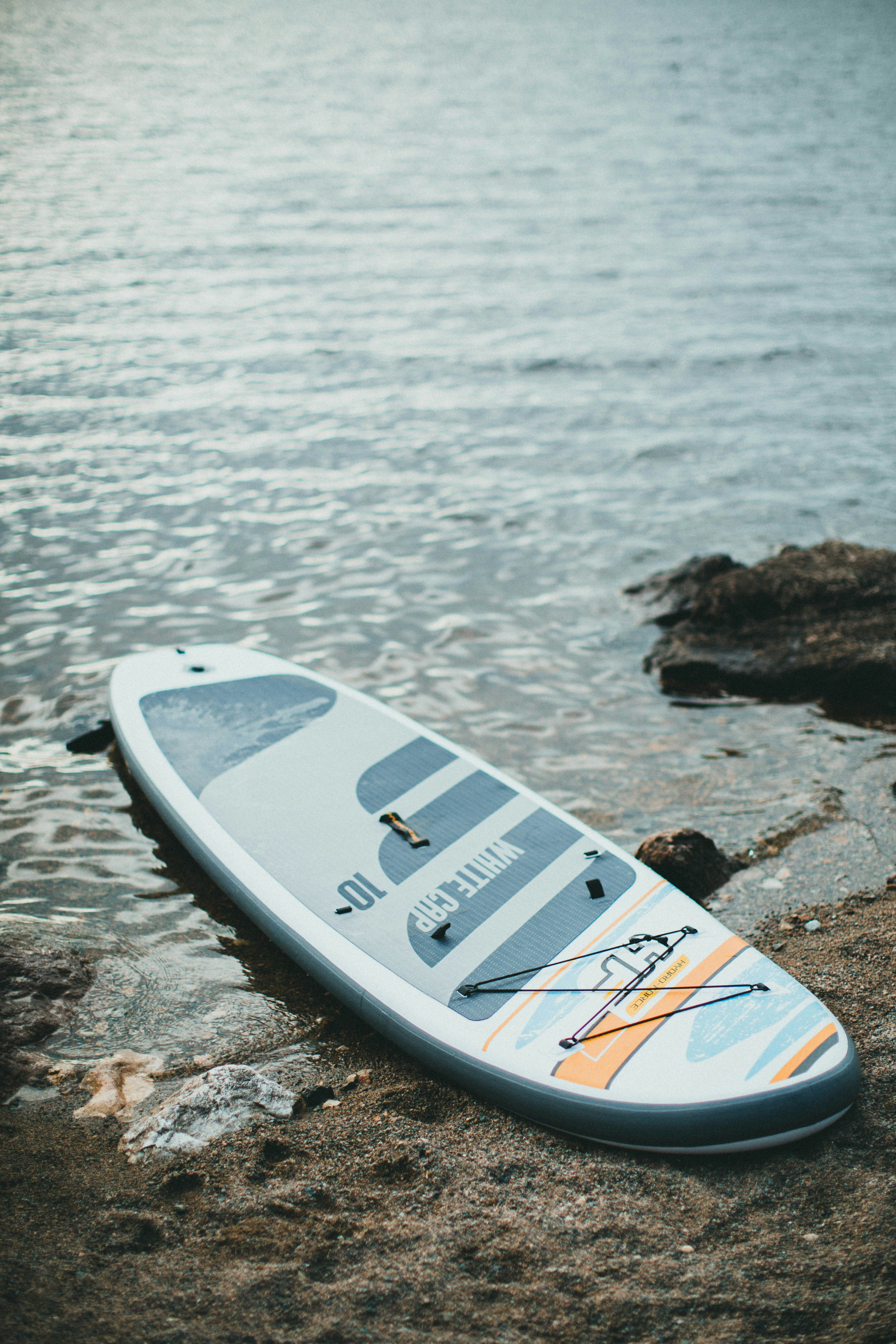 Standup Surfboard Resting Along Pebbled Shore Under Calm Light