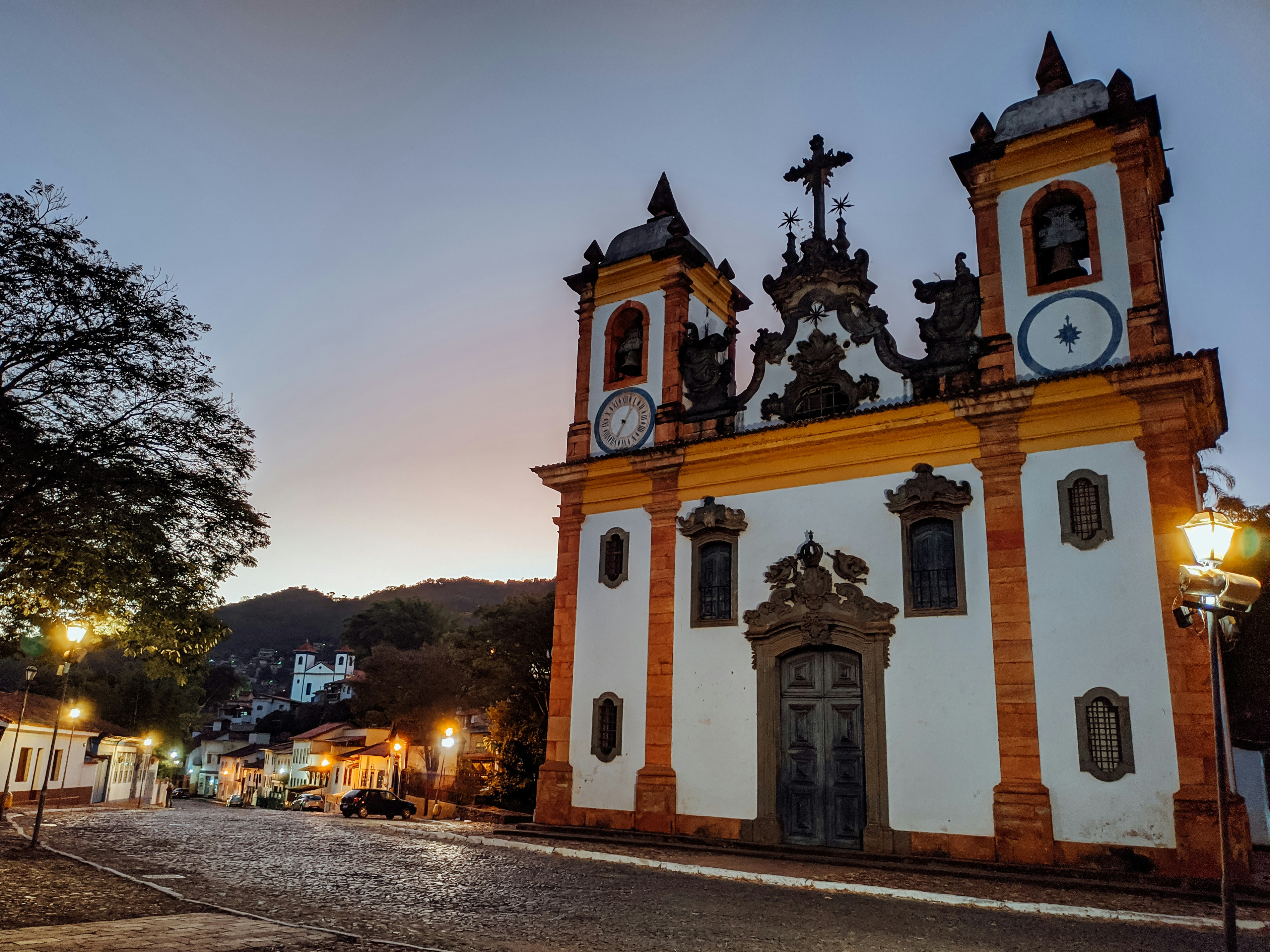 Historic church illuminated by warm streetlights at dusk, with a serene sky in the background.