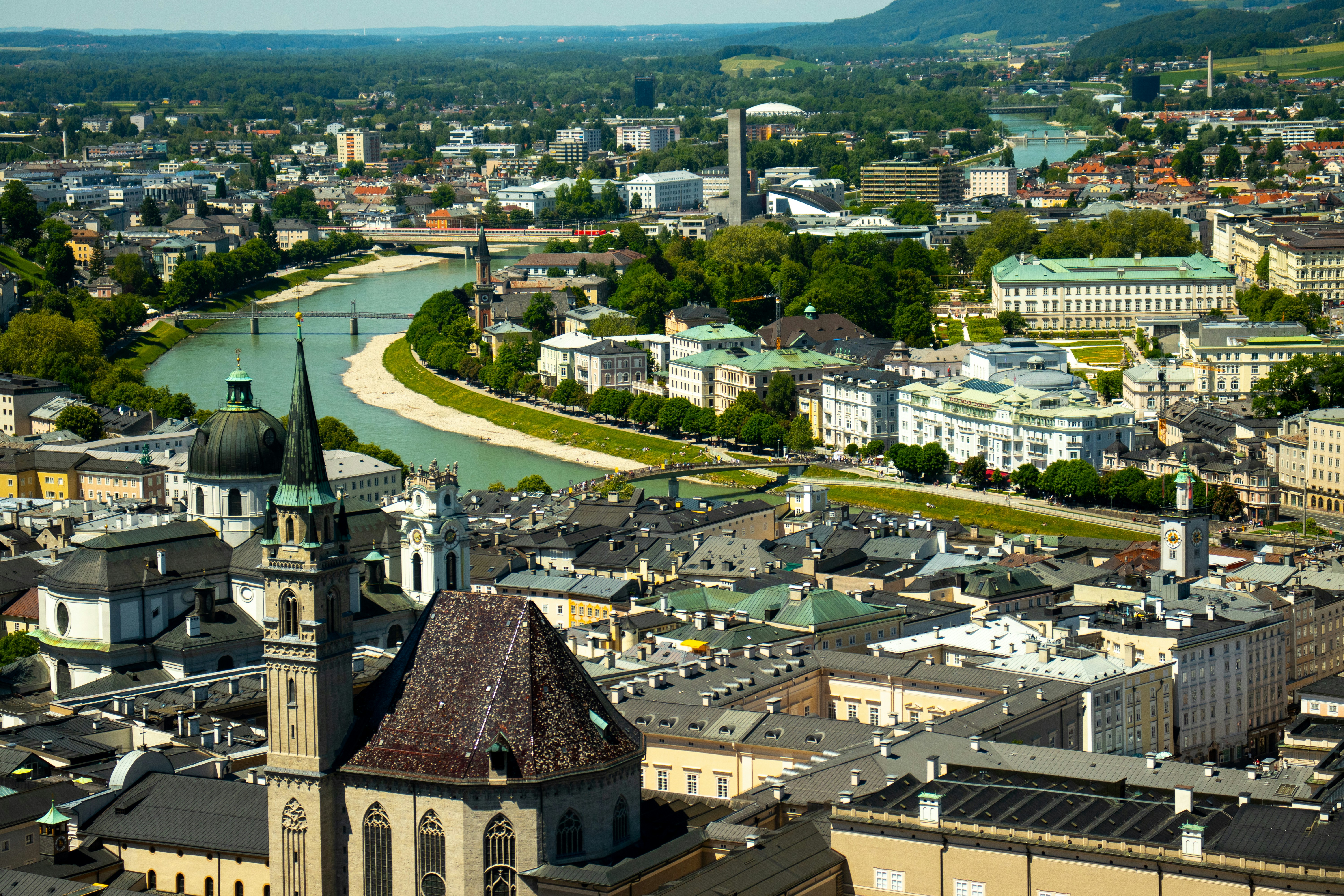 Aerial perspective of urban architecture with a winding river and distant hills under clear skies.