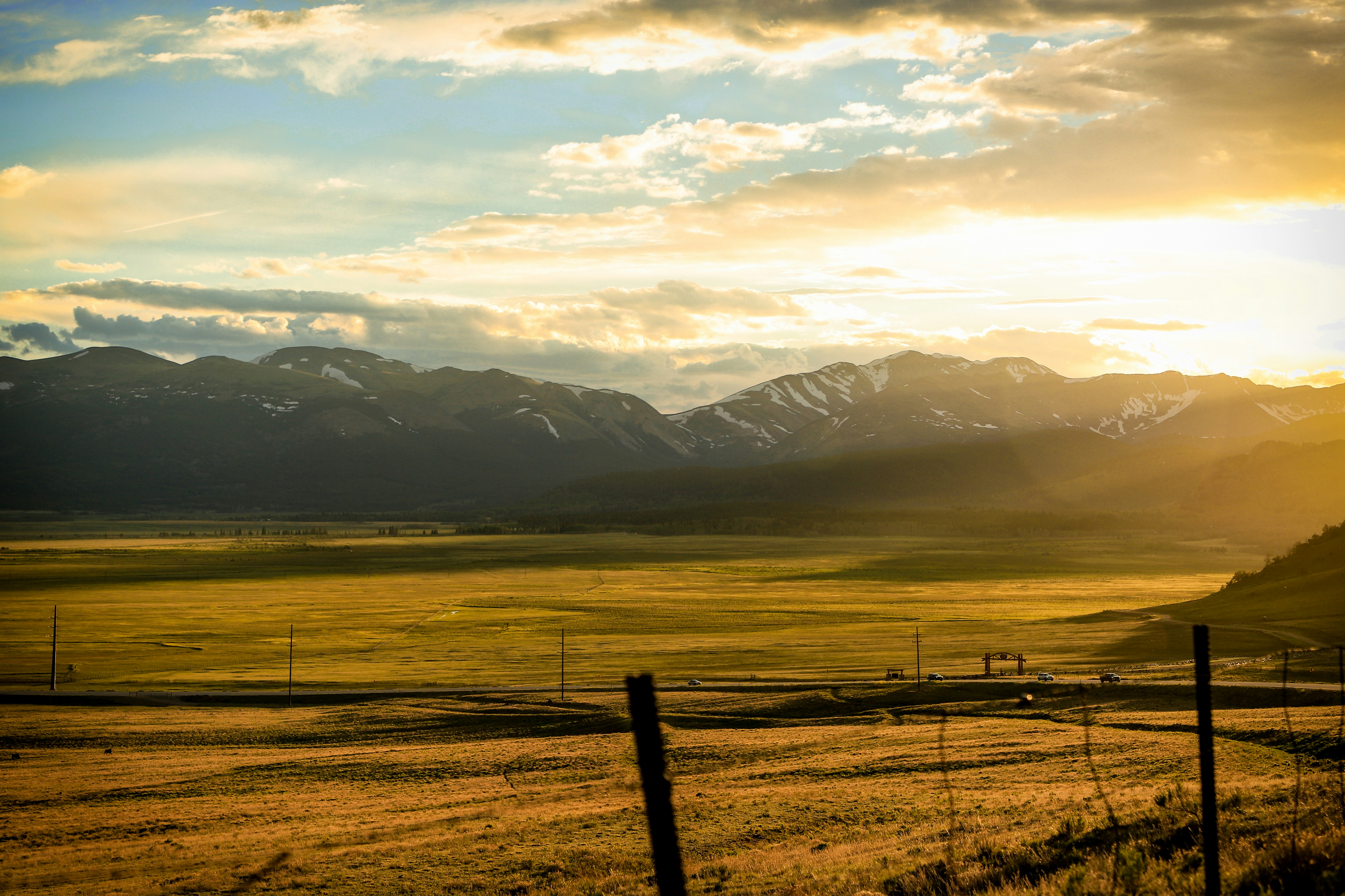 Sunlit valley with distant mountains under a partially cloudy sky at sunset.