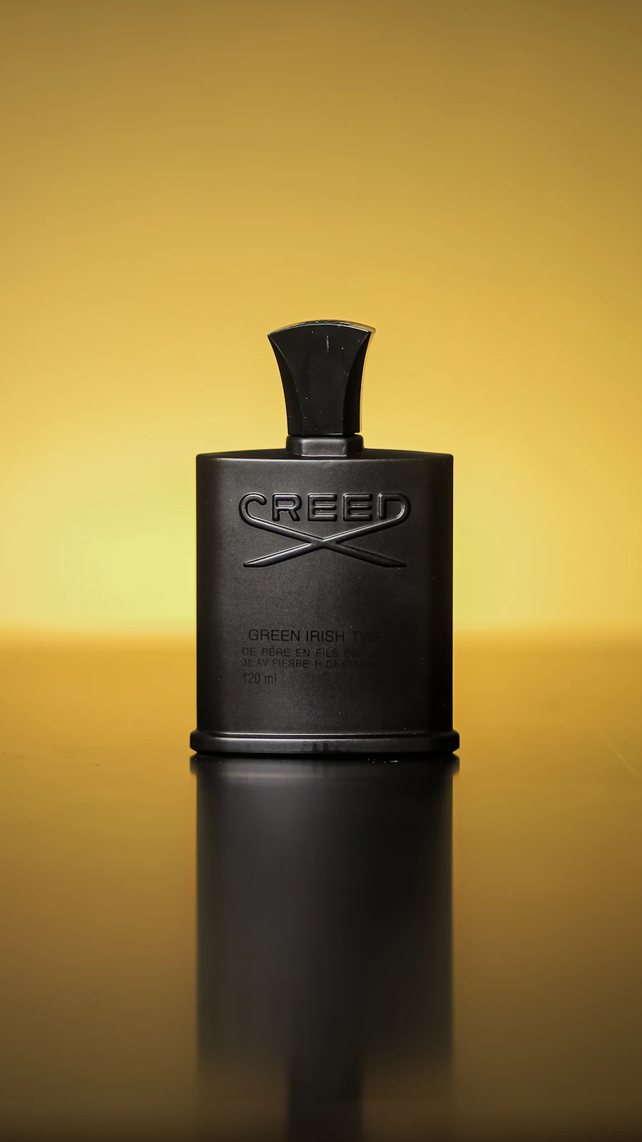 Black Creed Green Irish Tweed fragrance bottle centered against a warm yellow gradient background, with a glossy reflection below.