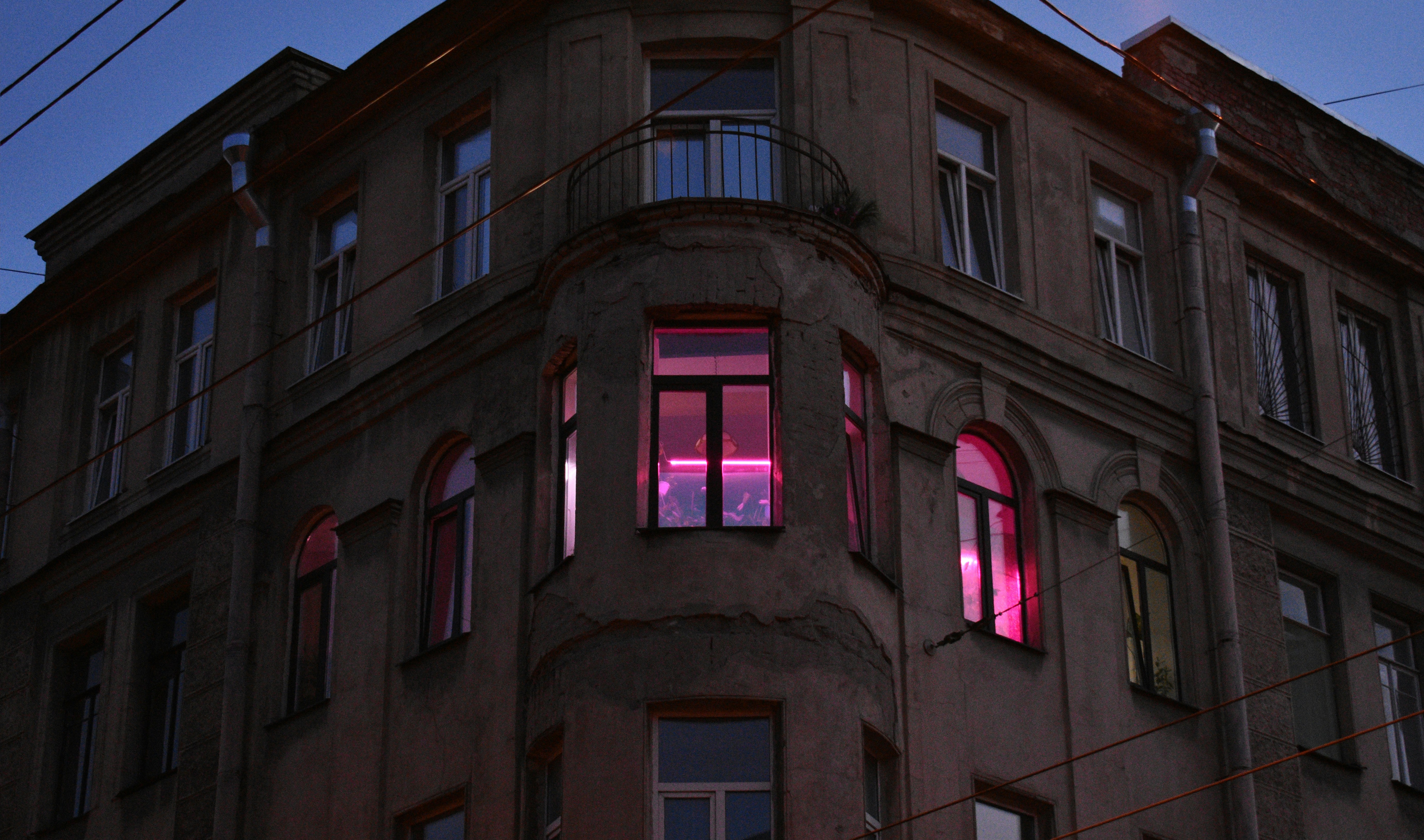 A corner building illuminated by vibrant pink lights from the windows, showcasing a blend of architecture and nightlife ambiance.