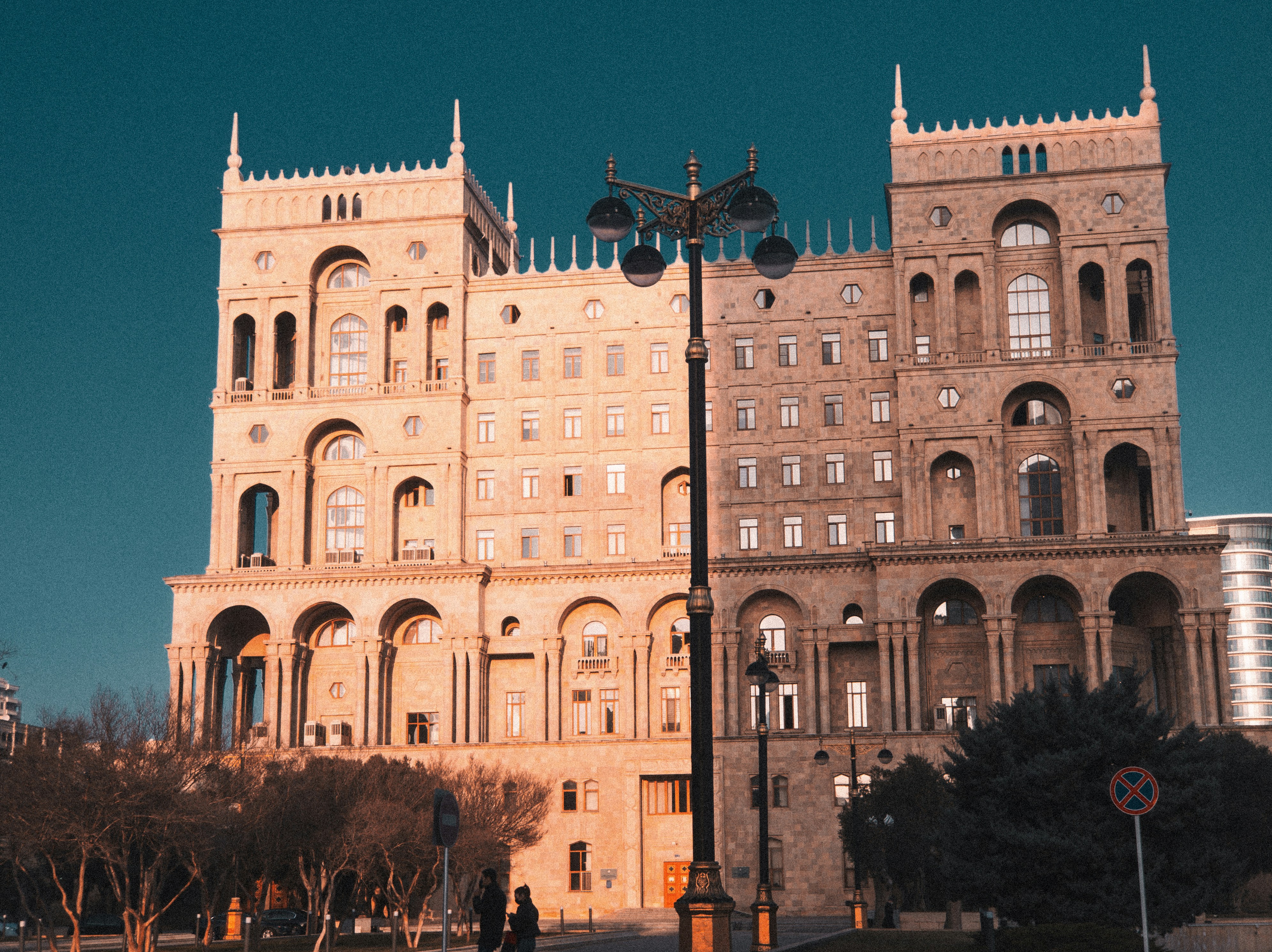 Historic twin-tower building photographed under a clear blue sky, centered by a vintage street lamp in the foreground.