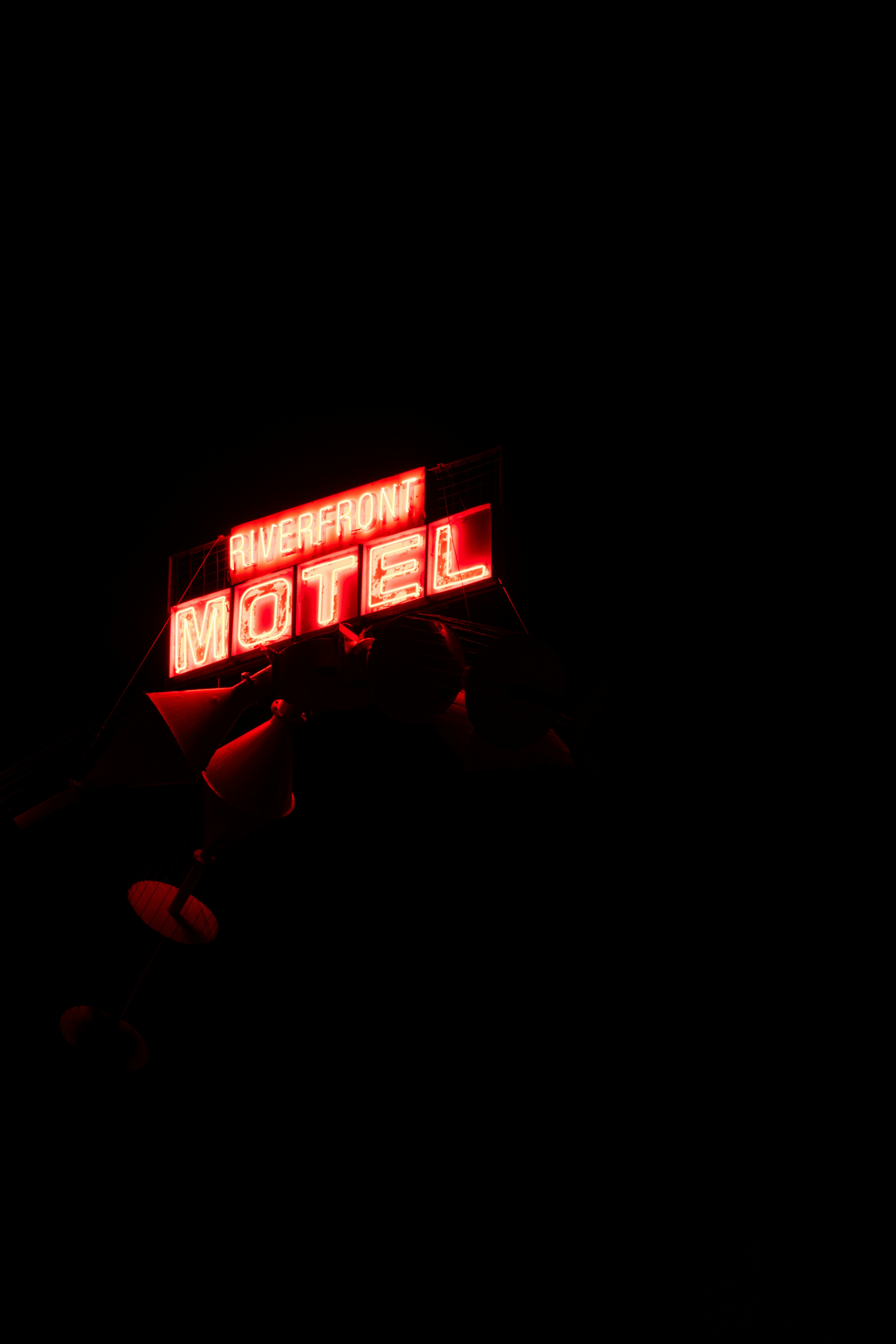 Bright red neon sign of the Riverfront Motel against a dark backdrop, highlighting vintage roadside aesthetics.