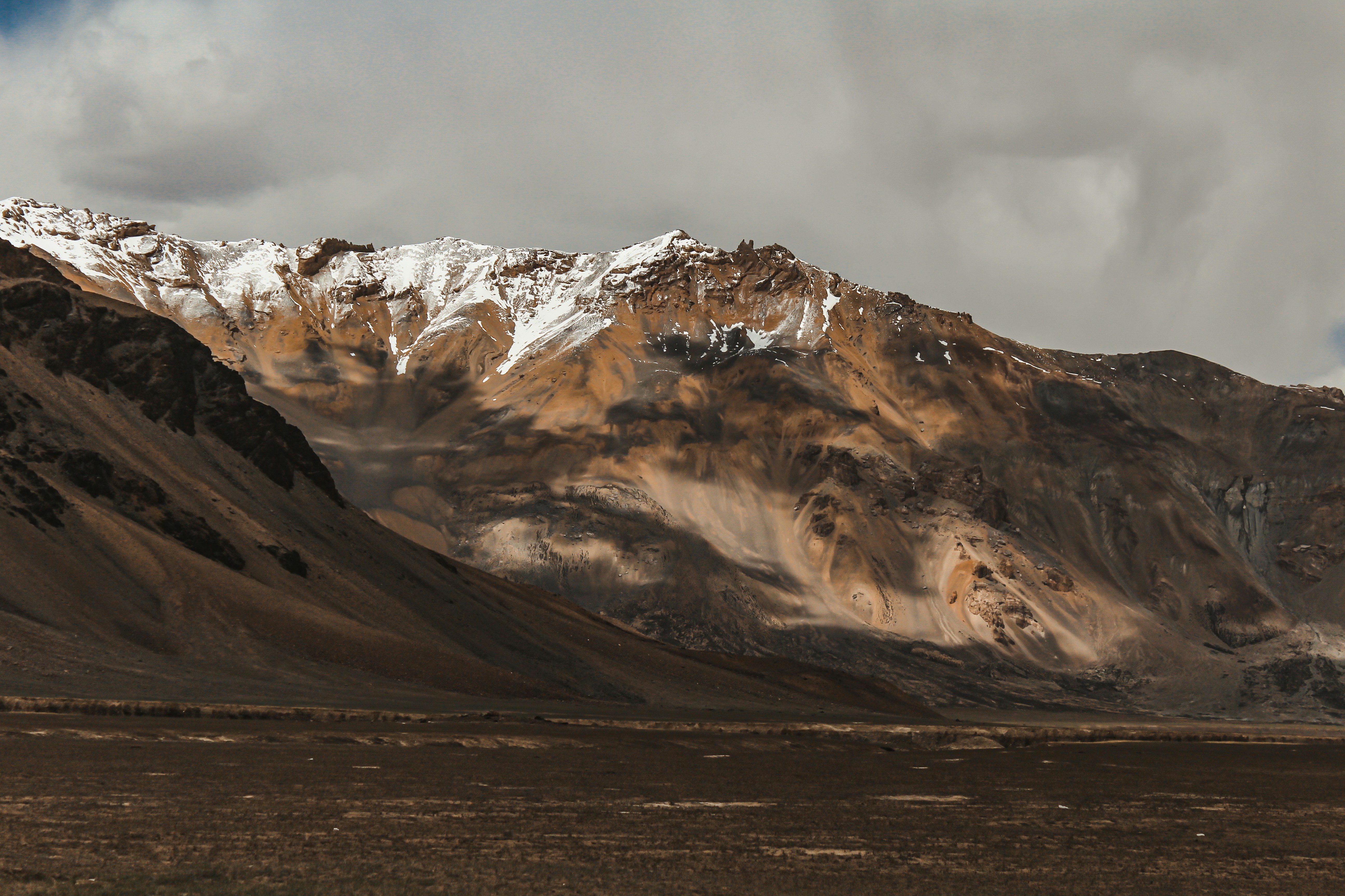 Snow-dusted mountain range beneath a cloudy sky during daytime.