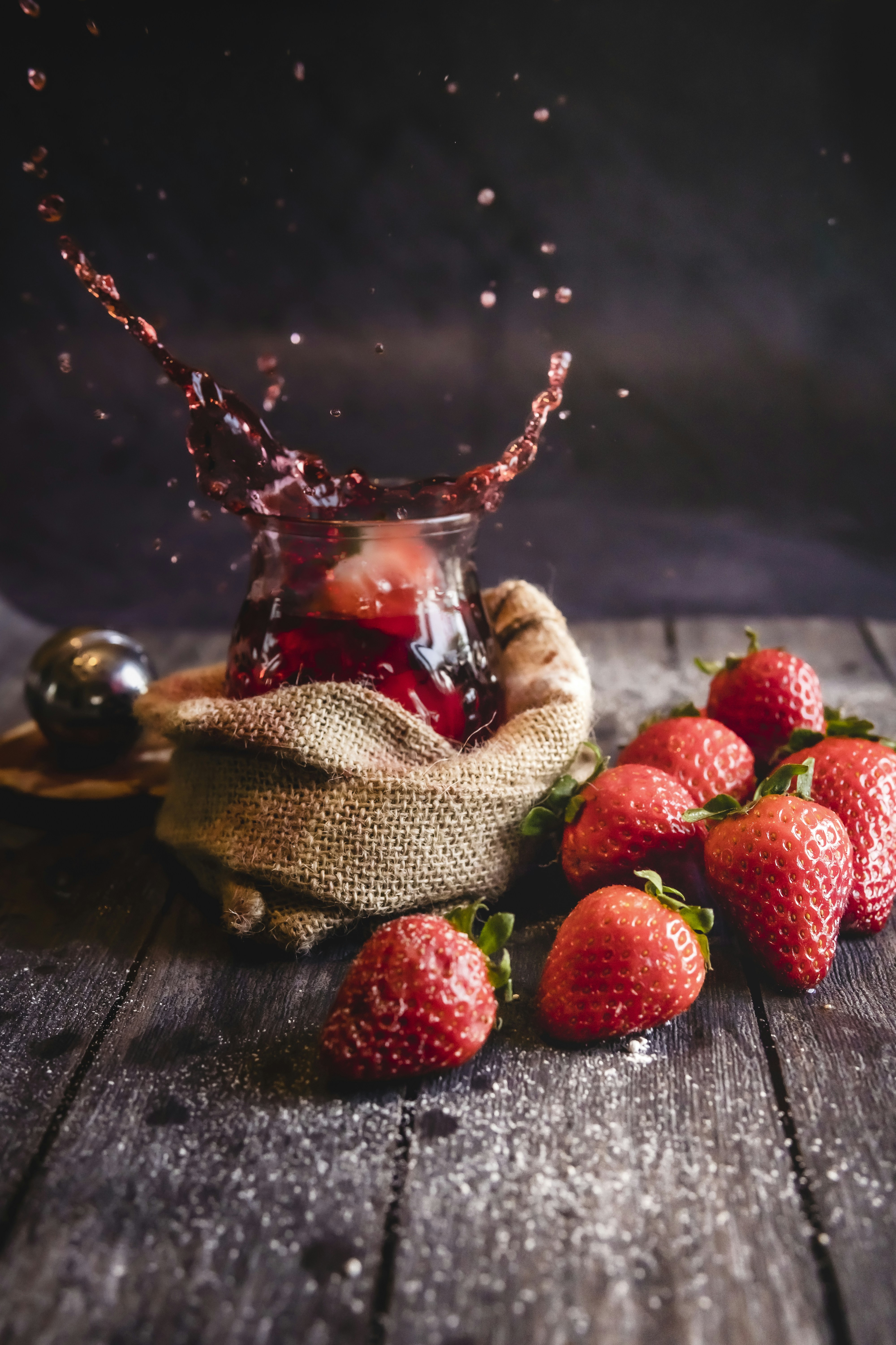 Splash of Berry Elixir: A Glass Jar Amid Fresh Strawberries on a Rustic Surface