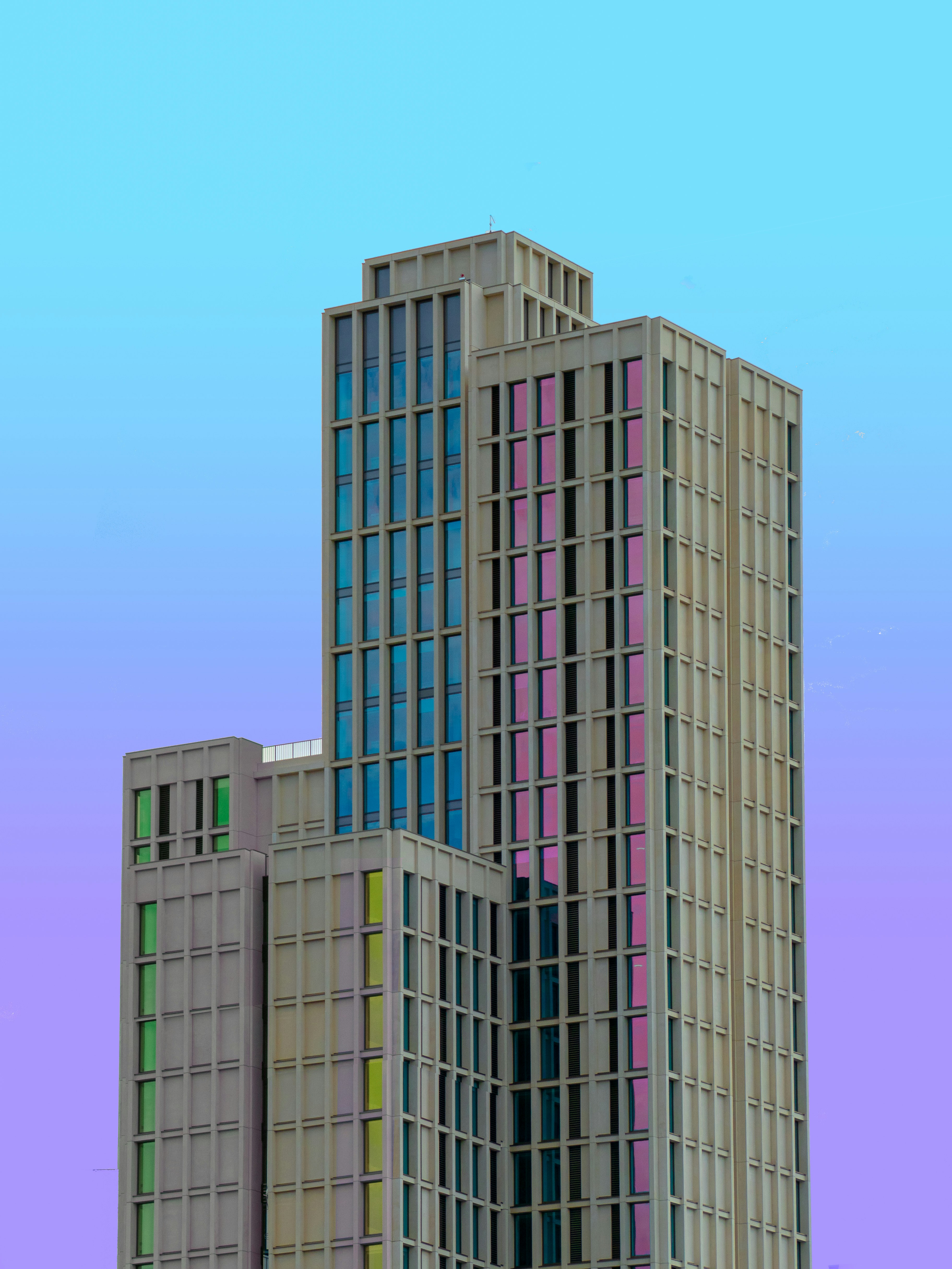 A contemporary skyscraper with colorful glass panels against a gradient sky. The design showcases a blend of geometric shapes and vibrant hues.