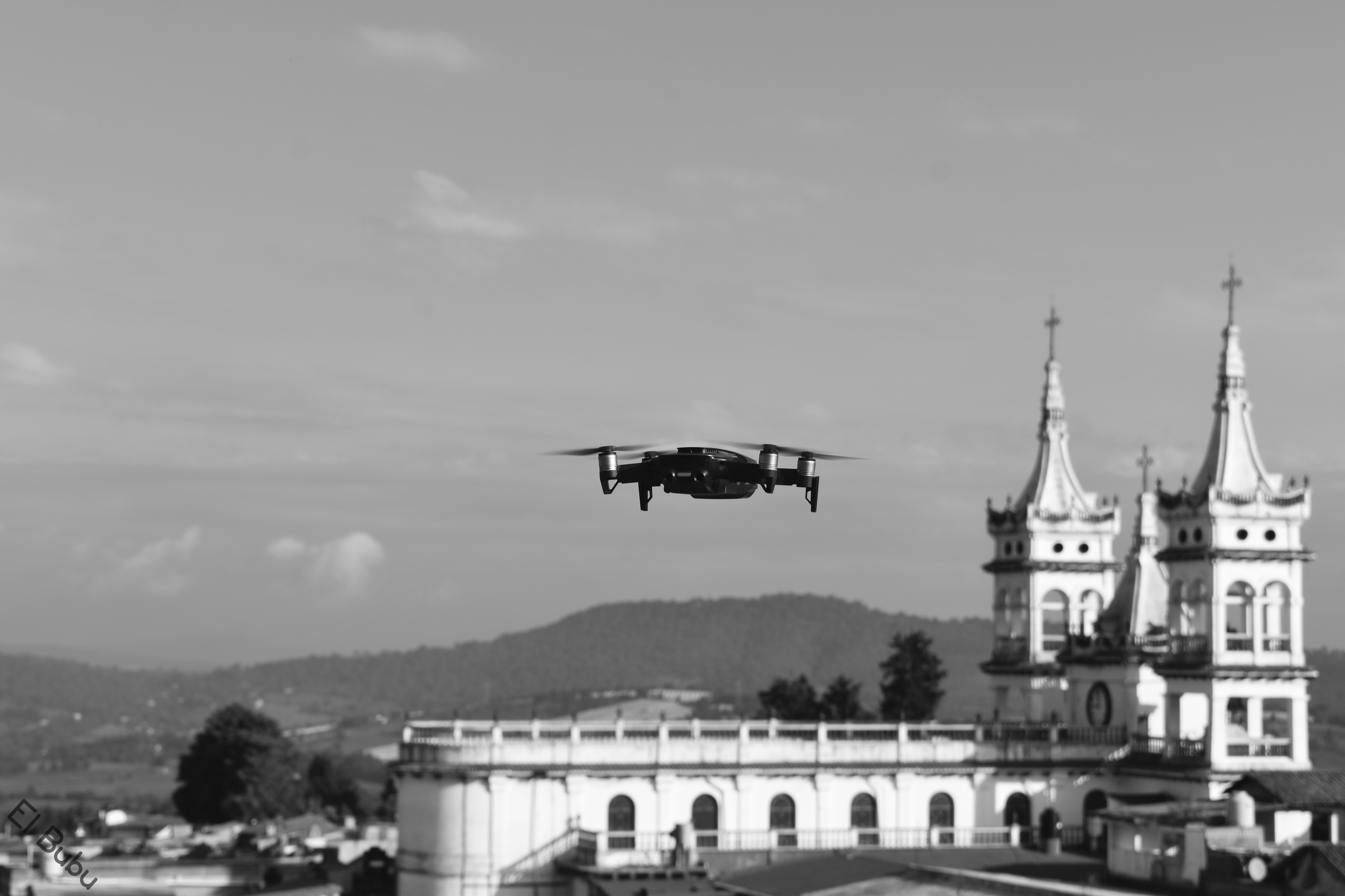 Drone hovering near ornate twin spires of a historic building with distant hills under a clear sky.