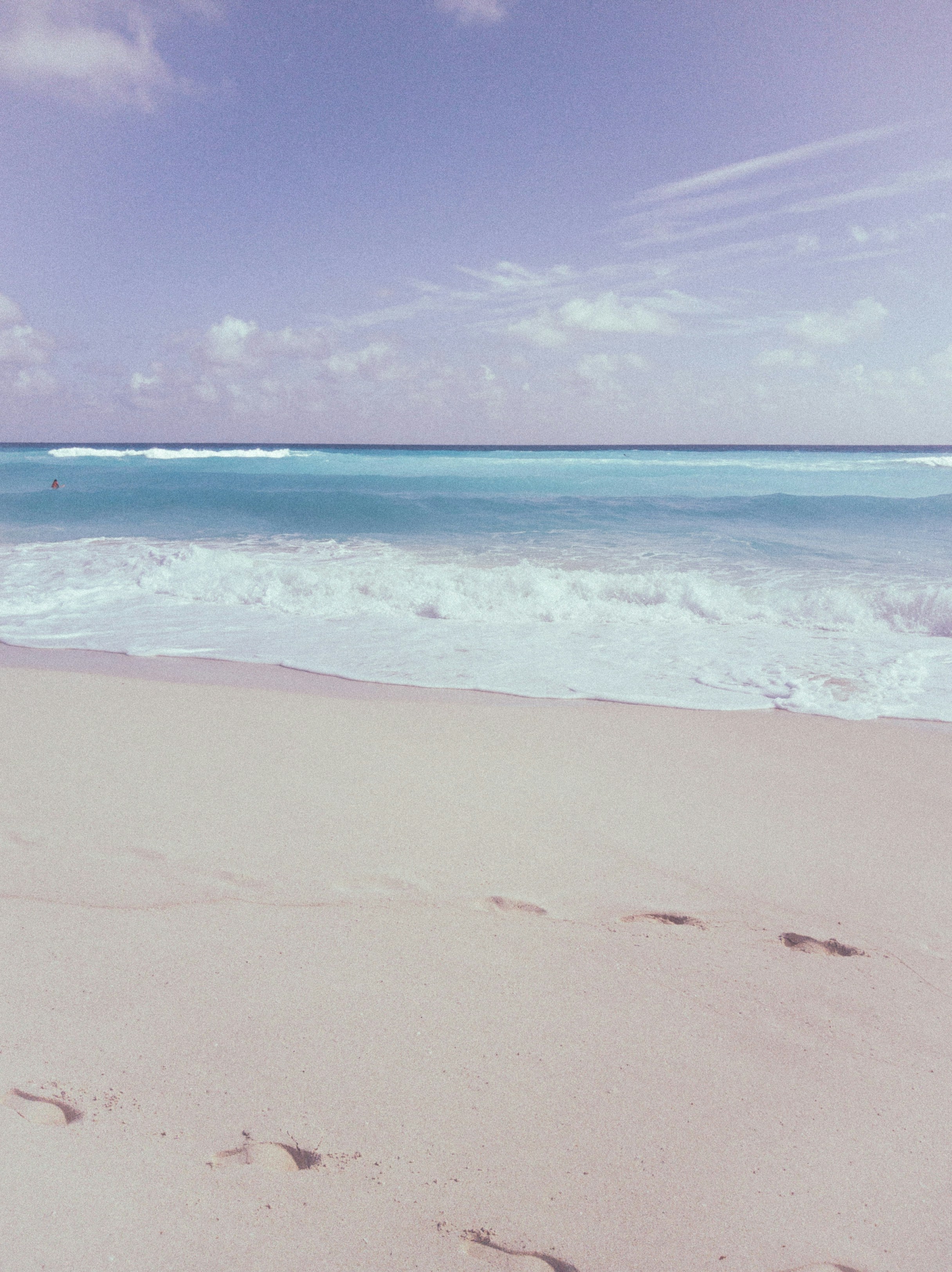 Pastel beach scene captured in a photograph, with gentle waves on a pale sand shore beneath a serene sky.