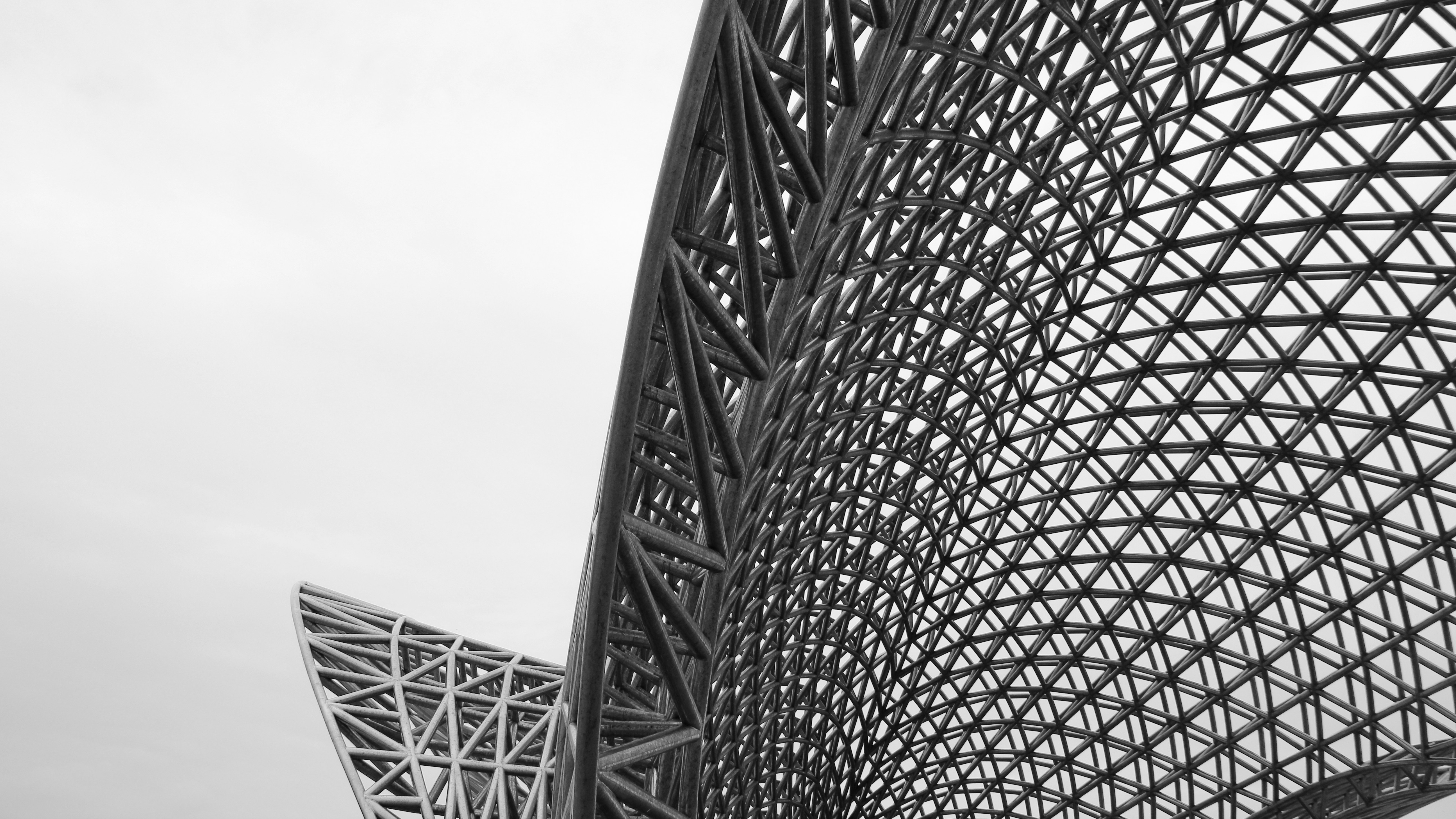 Curved steel lattice structure against a cloudy sky.