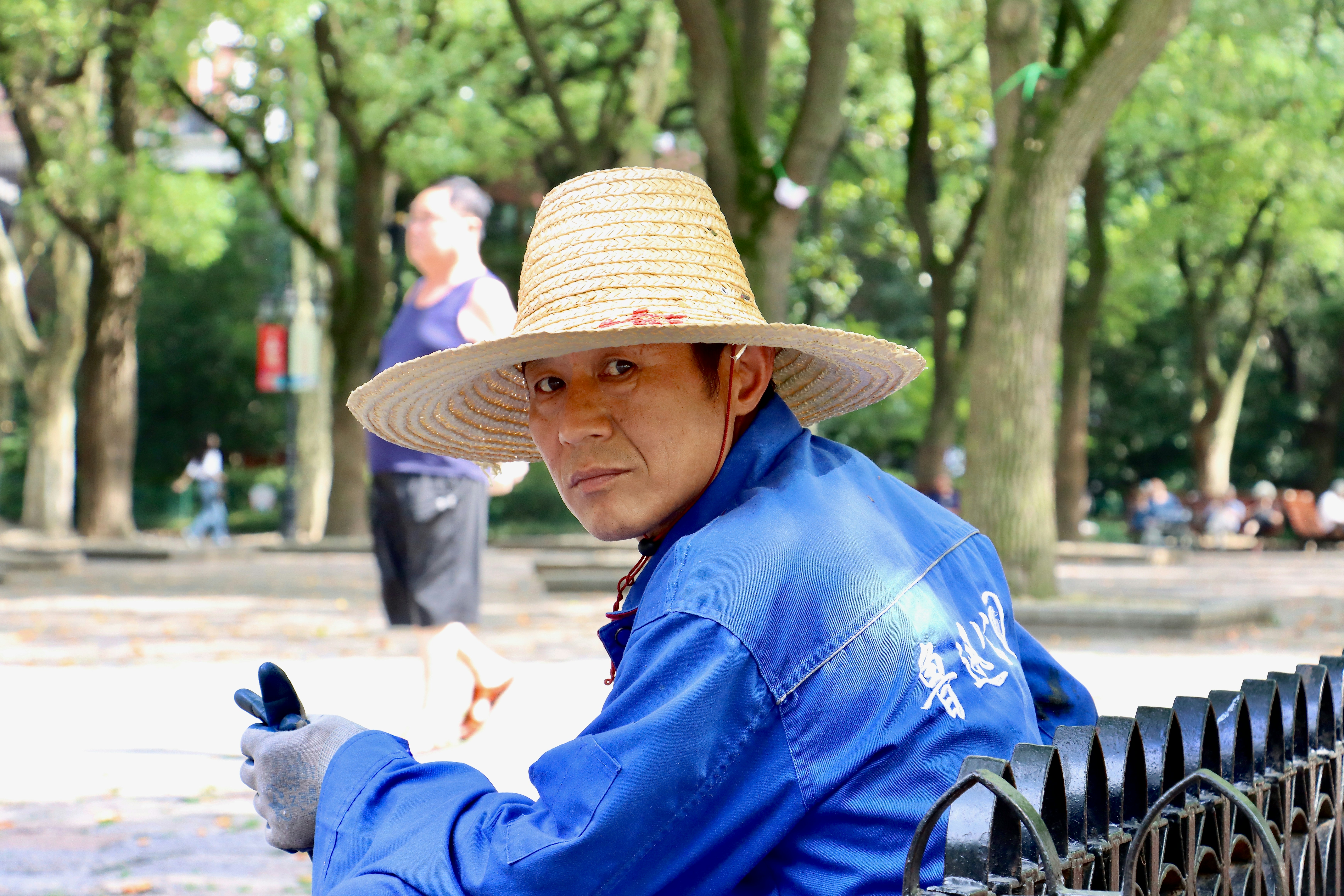 woman in blue jacket wearing brown straw hat sitting on bench during daytime