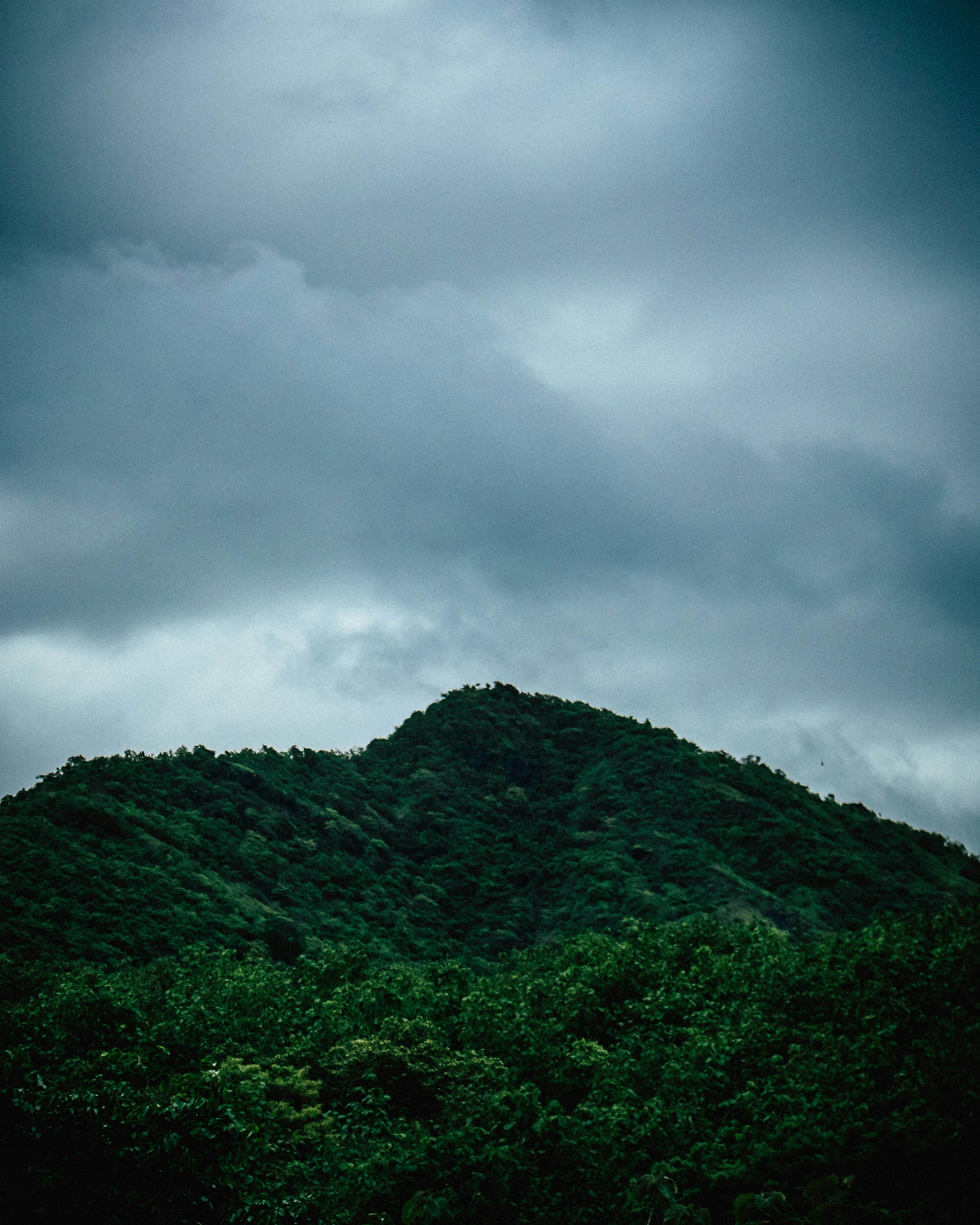 Lush green hills rise against a backdrop of dark, overcast skies, evoking a sense of mystery and tranquility.