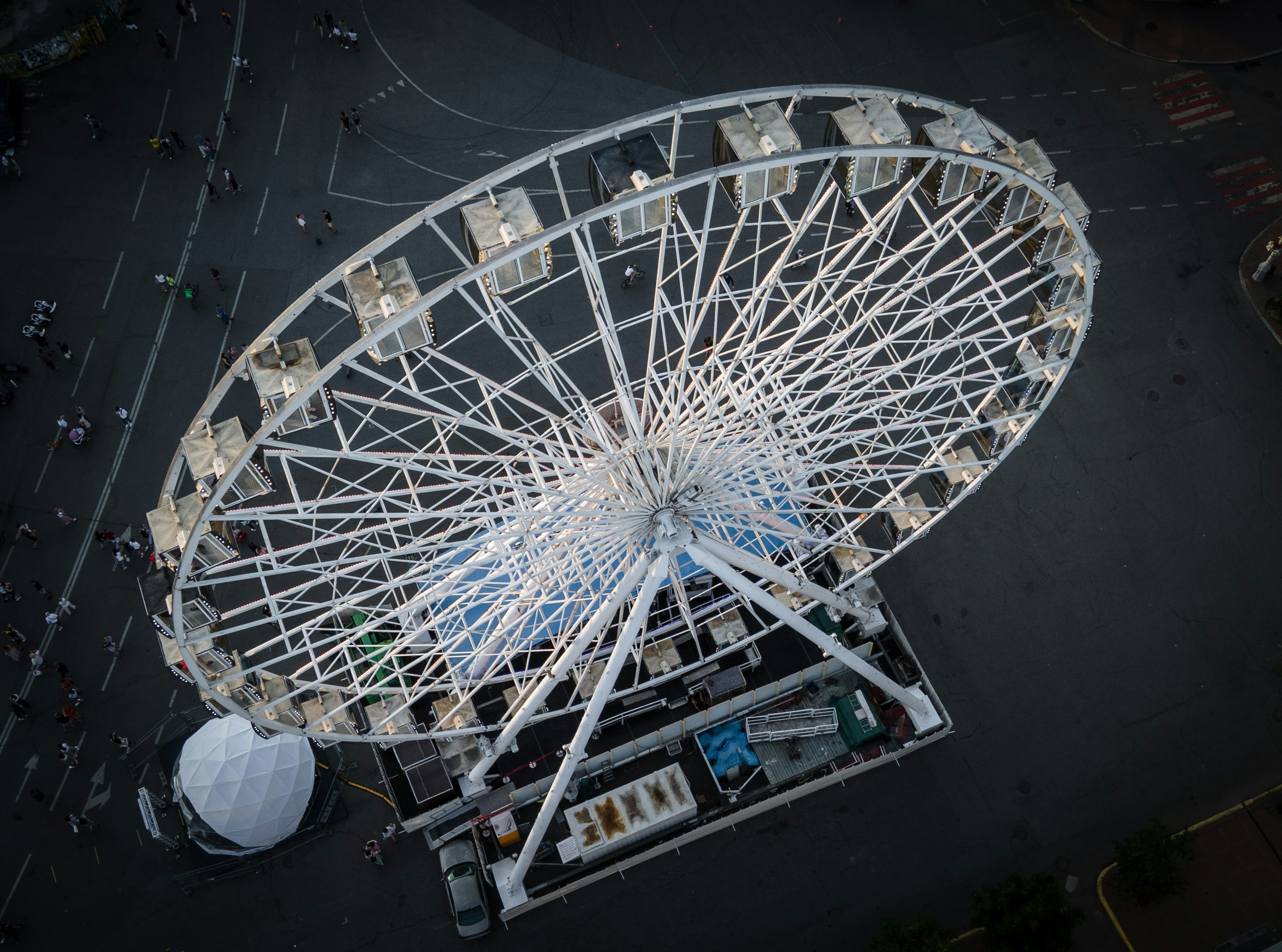 Aerial view of a Ferris wheel illuminated against the evening sky, showcasing its intricate structure and surrounding fairground activities.