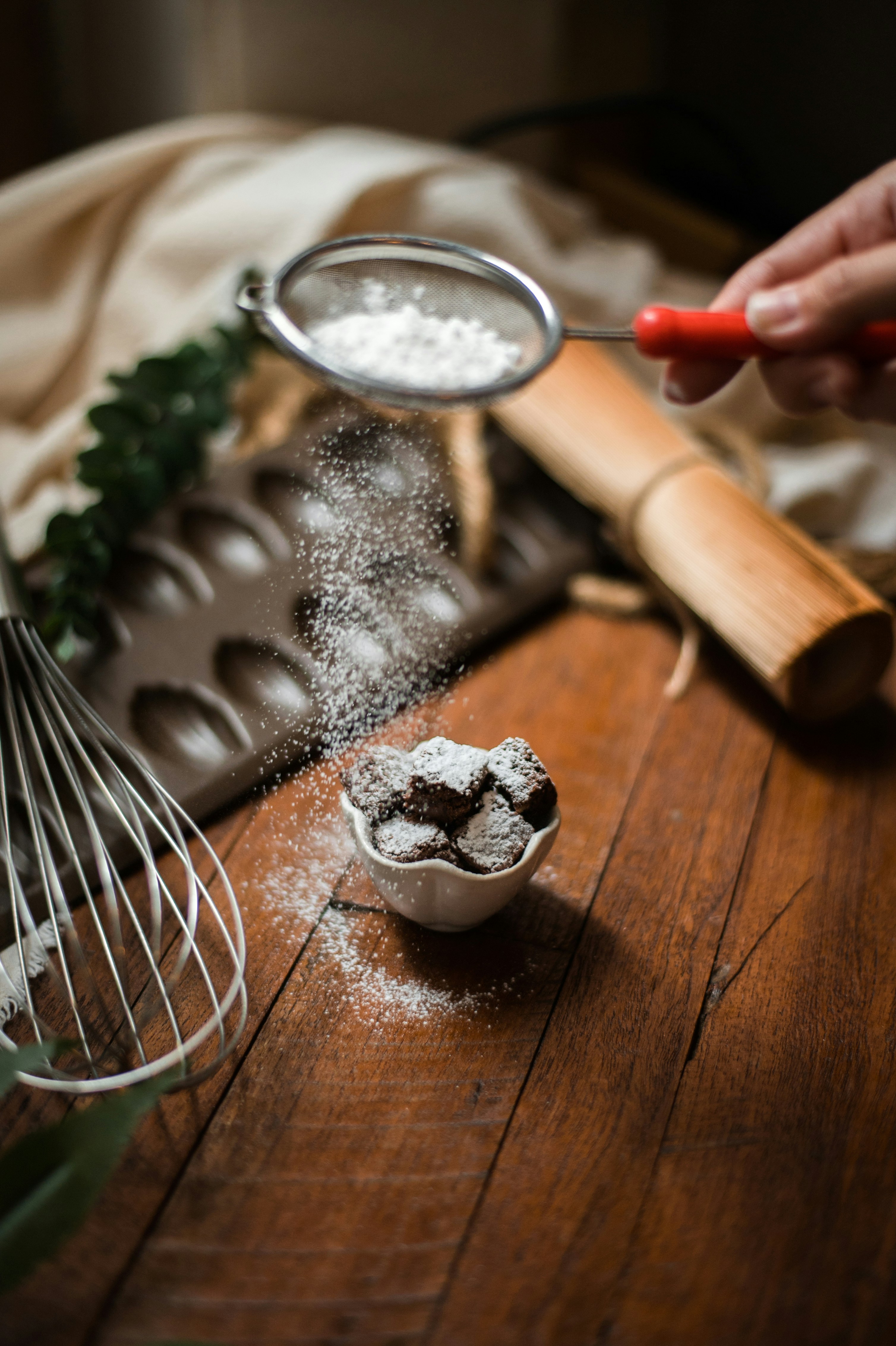 Small bowl of brownies being dusted with powdered sugar on a wooden table.