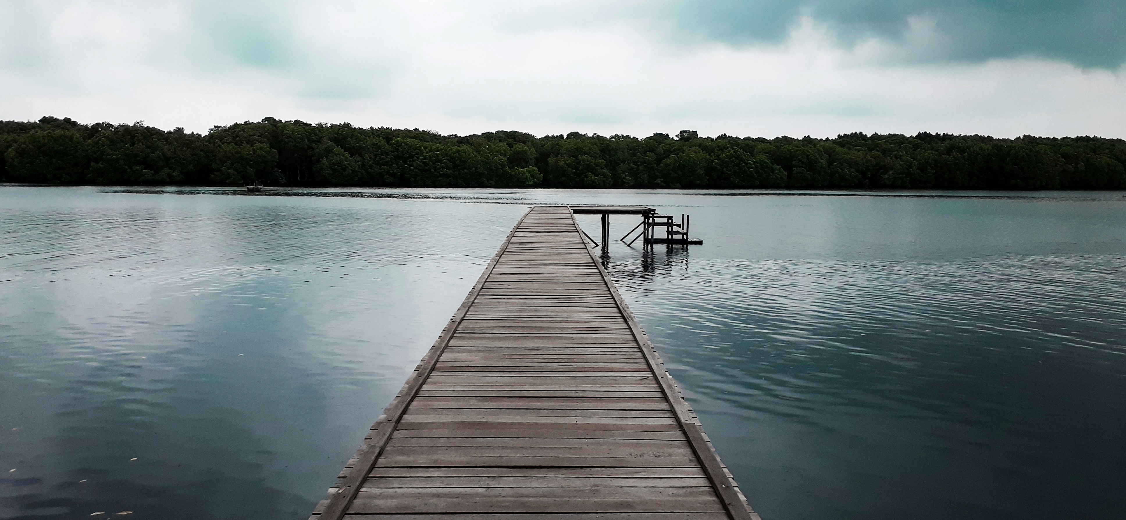 Wooden pier stretching into calm waters under a cloudy sky.