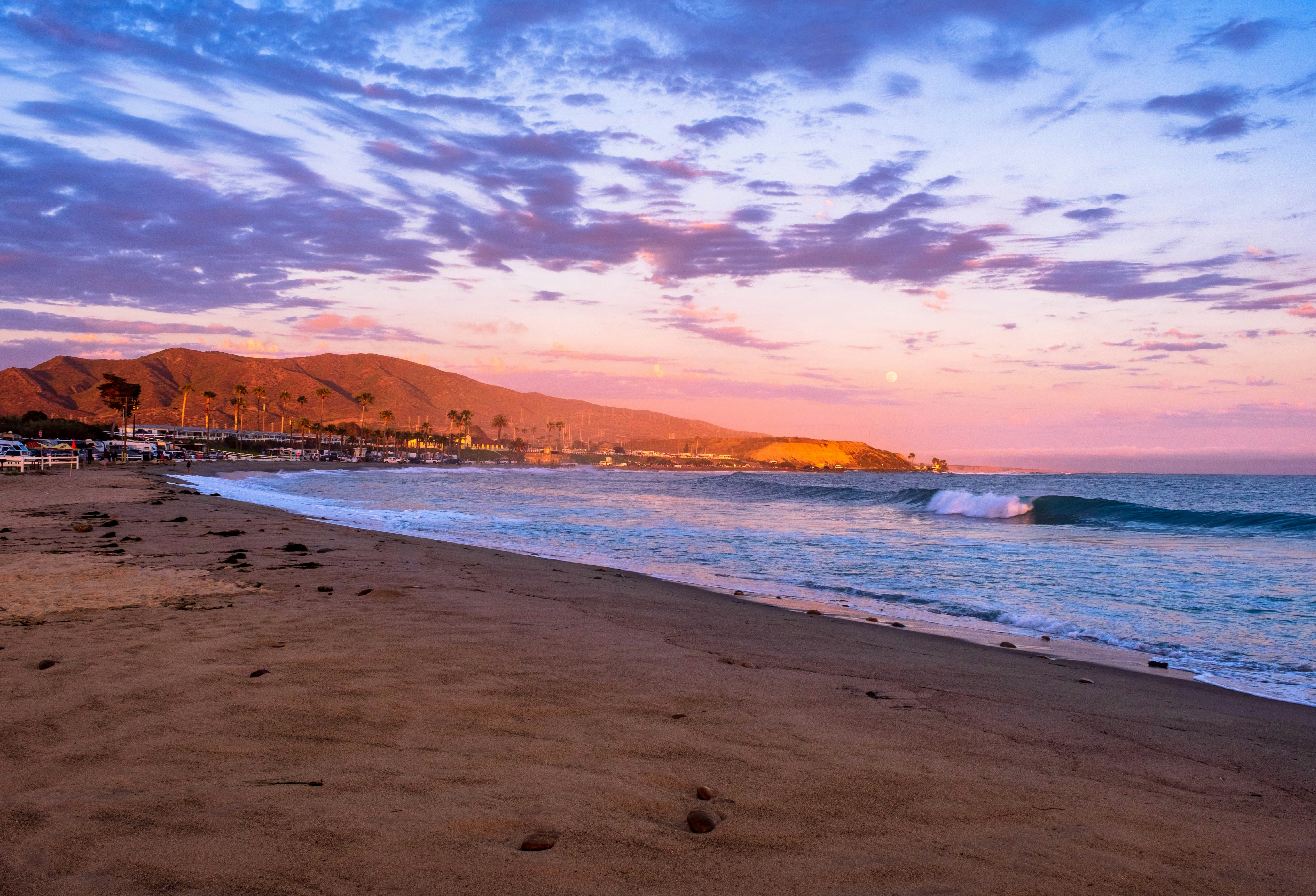 Vibrant sunset over a tranquil beach with gentle waves and distant hills under a colorful sky.