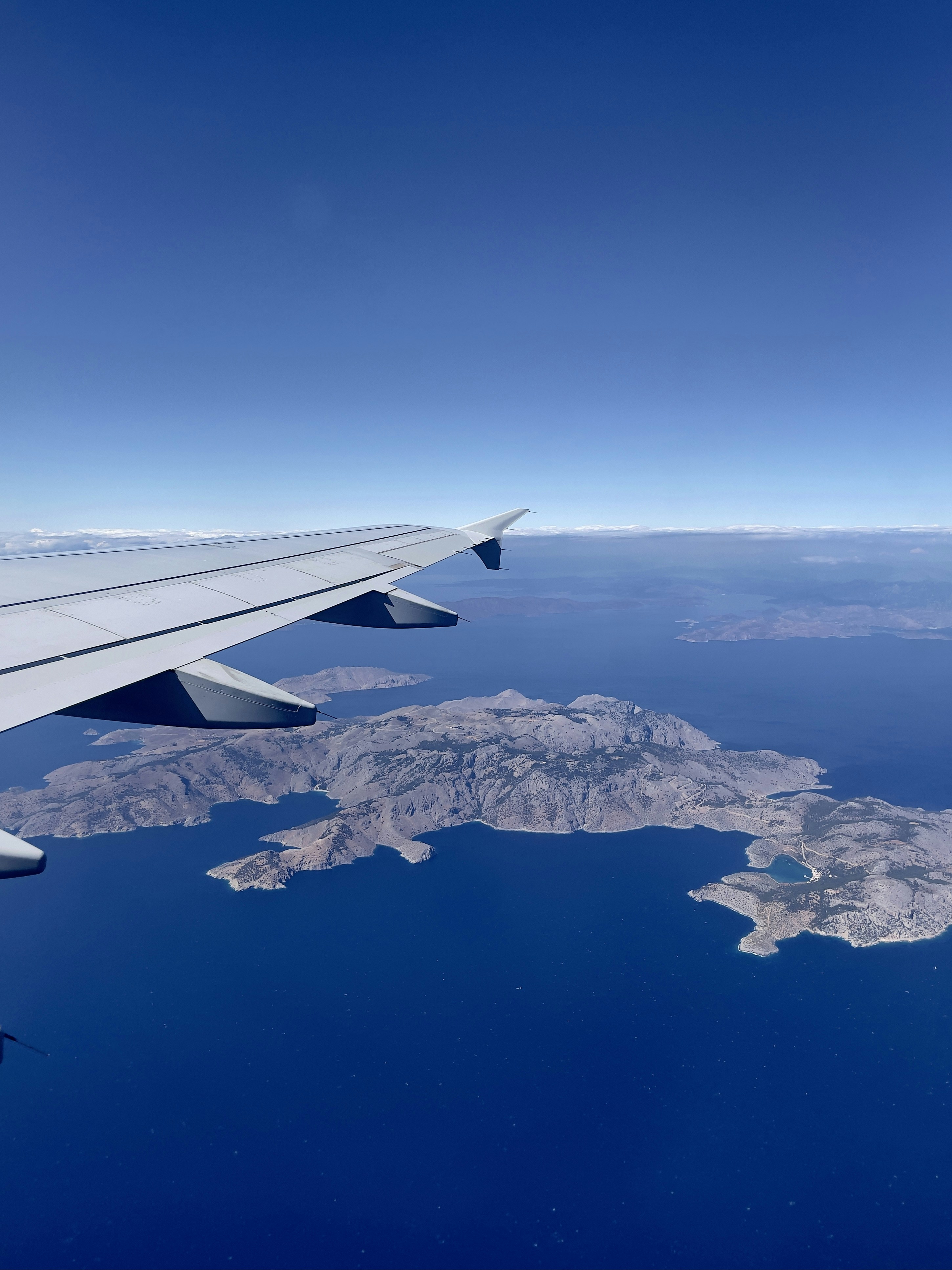 Airplane wing extending over a cluster of islands surrounded by deep blue waters under a clear sky.