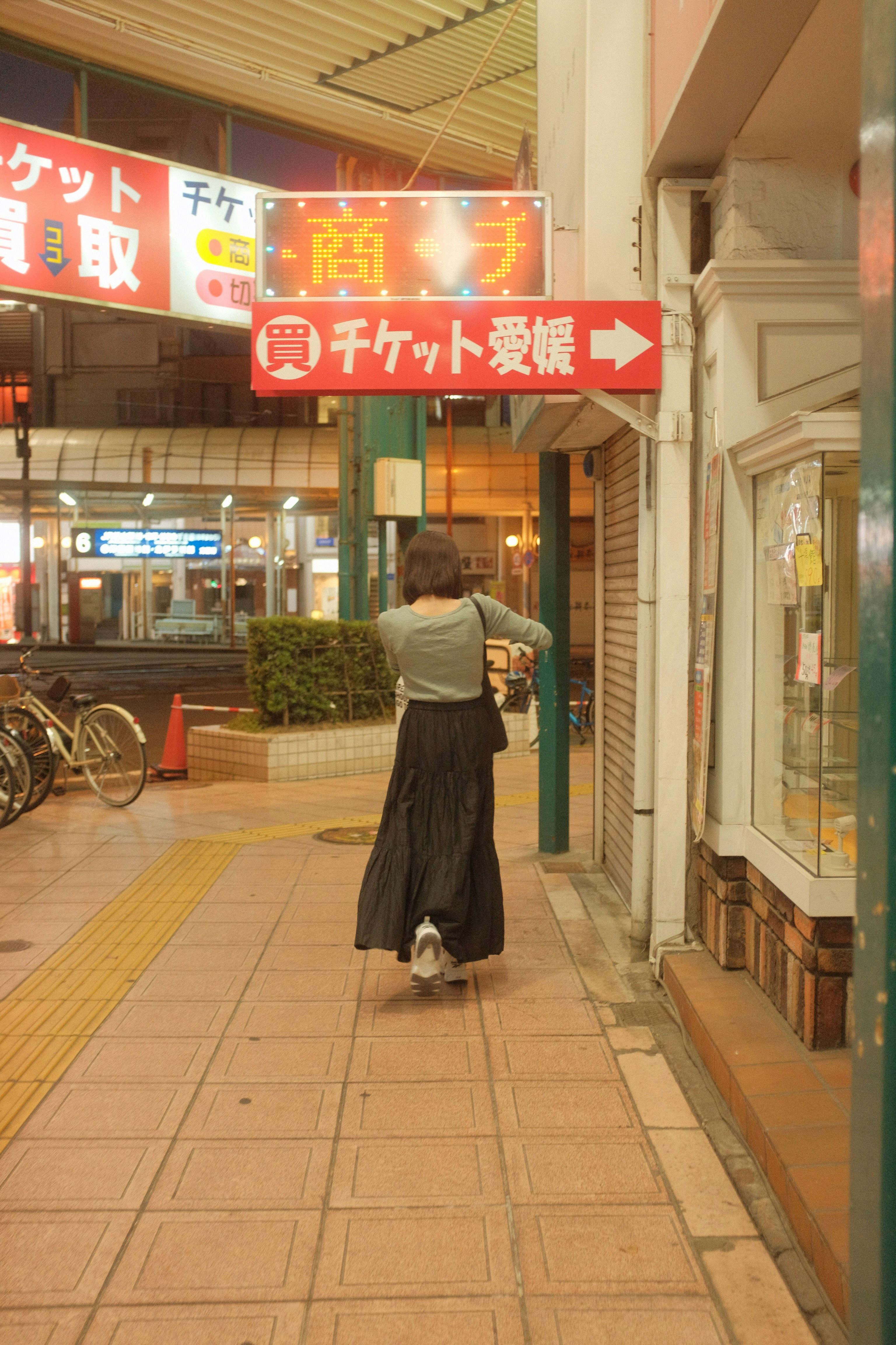 Neon Corridor: A Woman in a Long Skirt Walks Beneath Red Signage