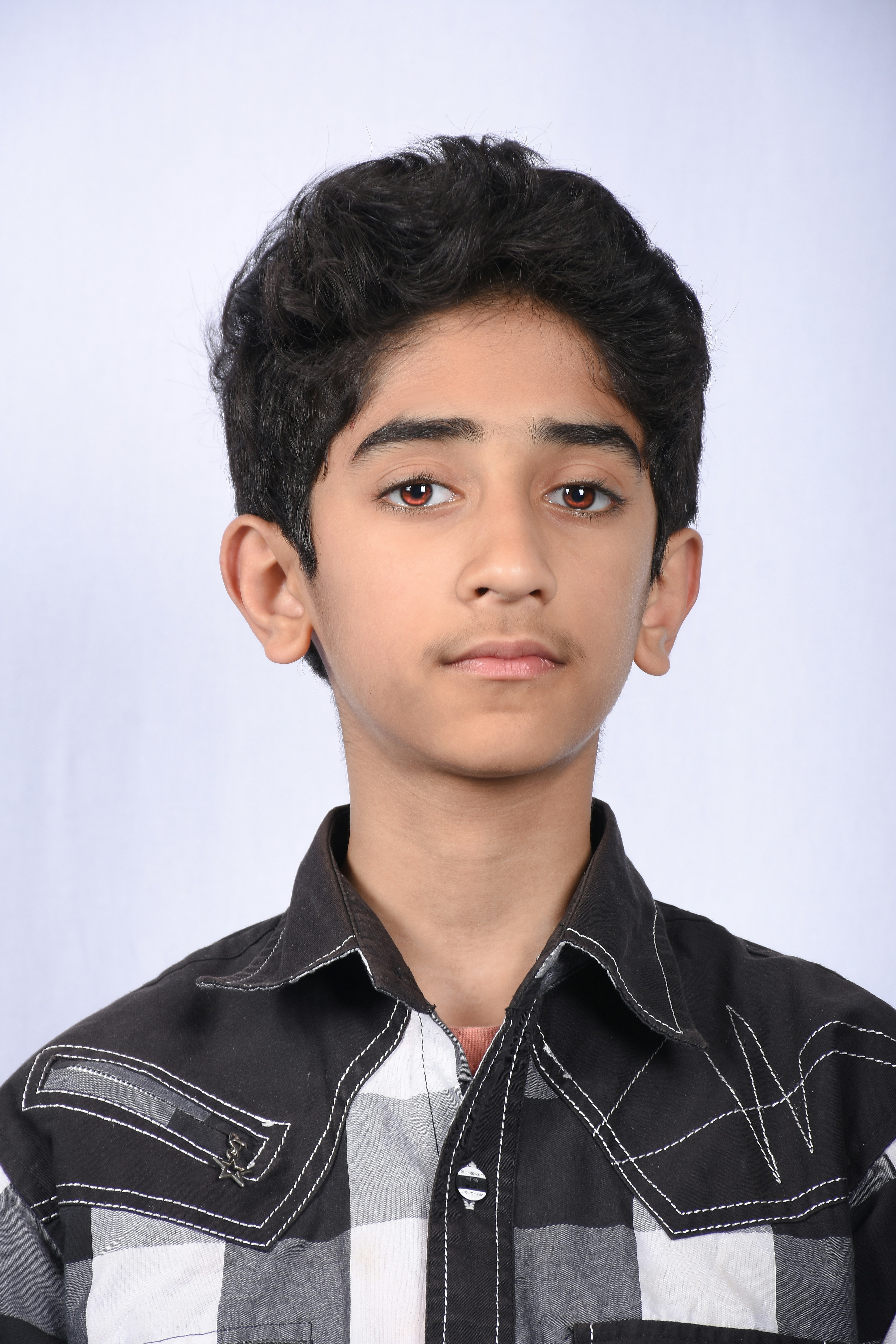 A young boy with a serious expression poses against a neutral backdrop, showcasing his stylish black and white checkered shirt.