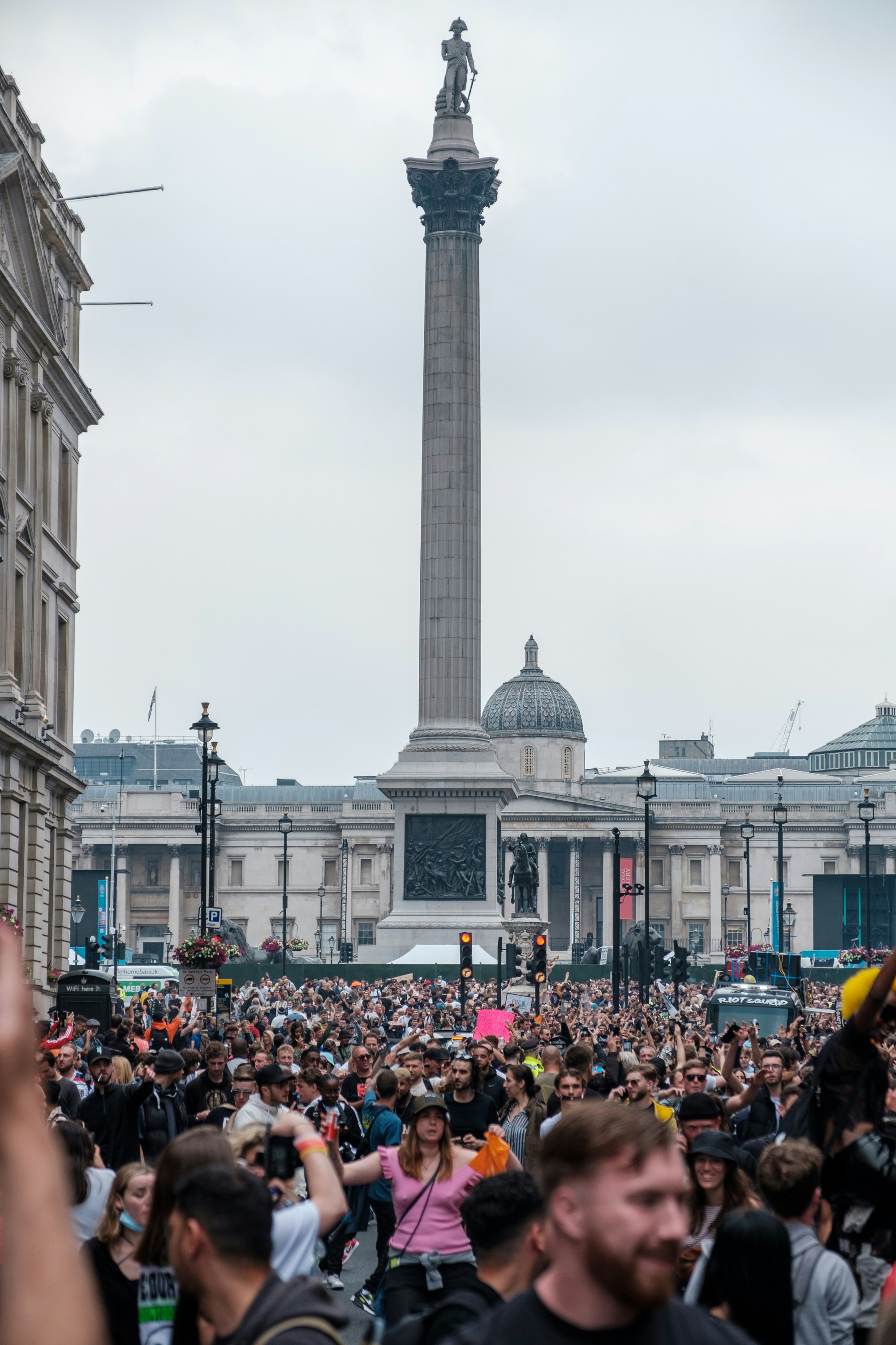 Crowd of people celebrating in Trafalgar Square, with Nelson's Column prominently rising in the background. 