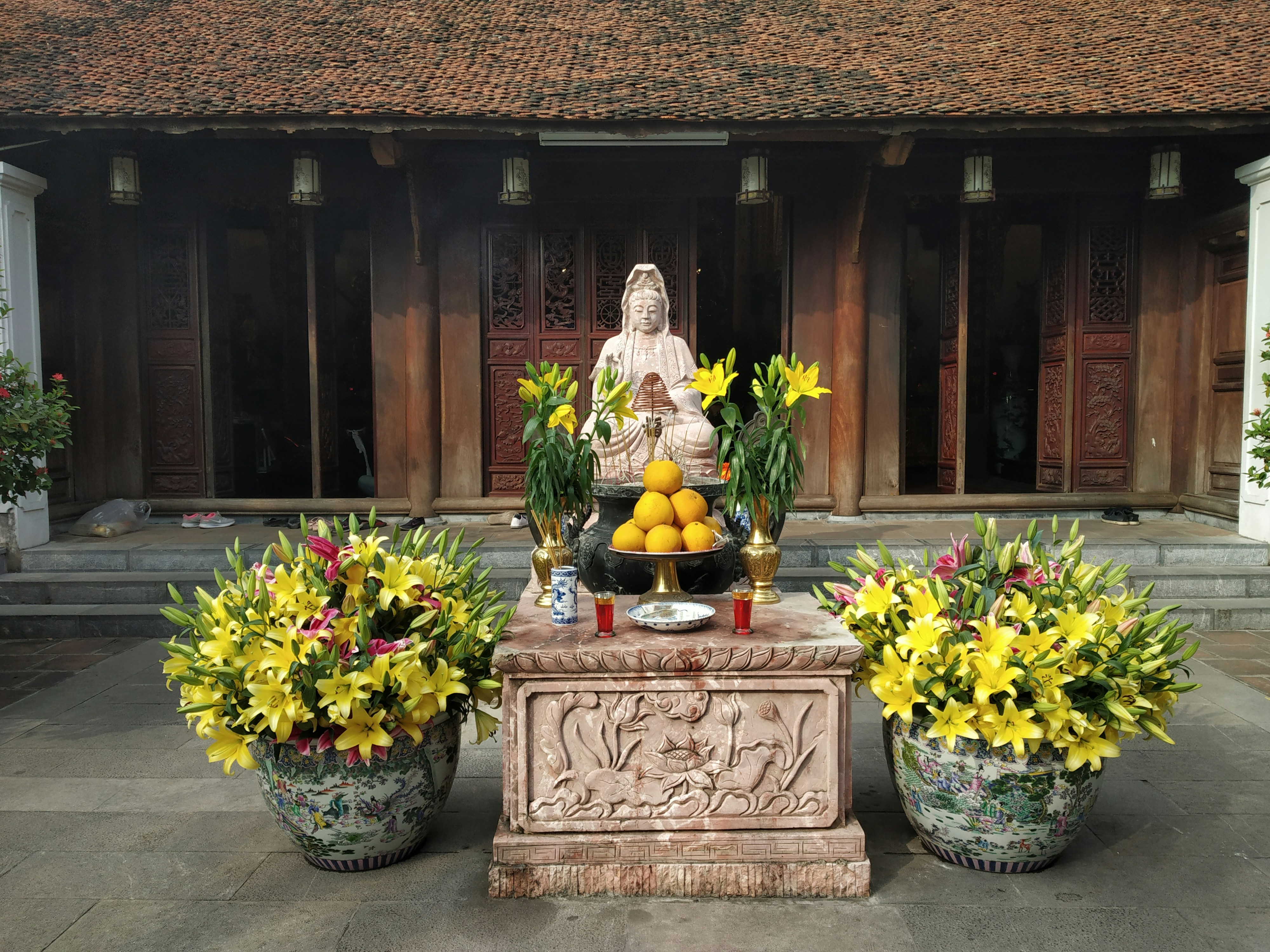 Stone statue surrounded by vibrant yellow flowers and fruits in a tranquil courtyard.
