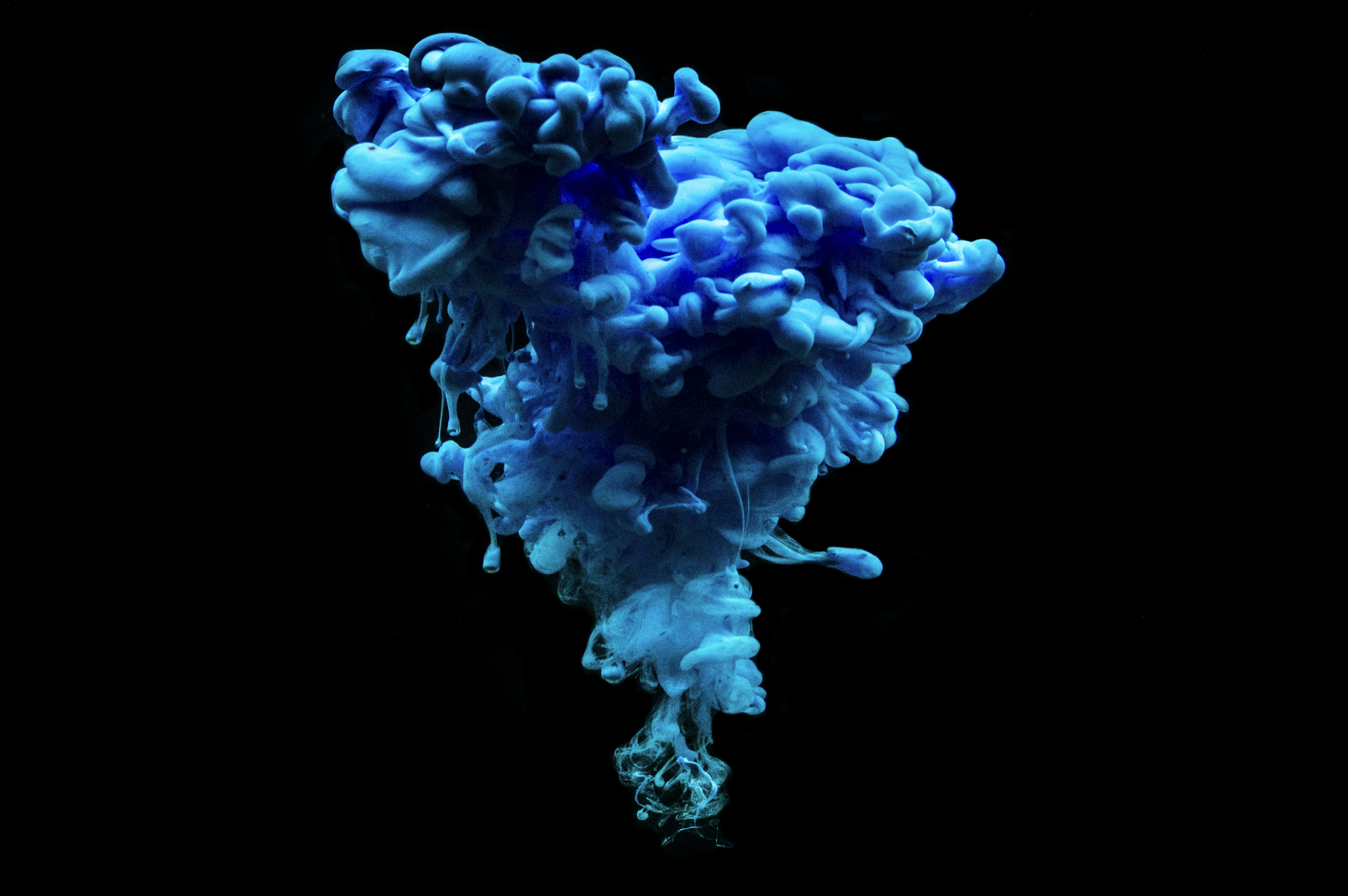 Vibrant blue ink swirling gracefully in water, creating a mesmerizing cloud-like formation against a black background.