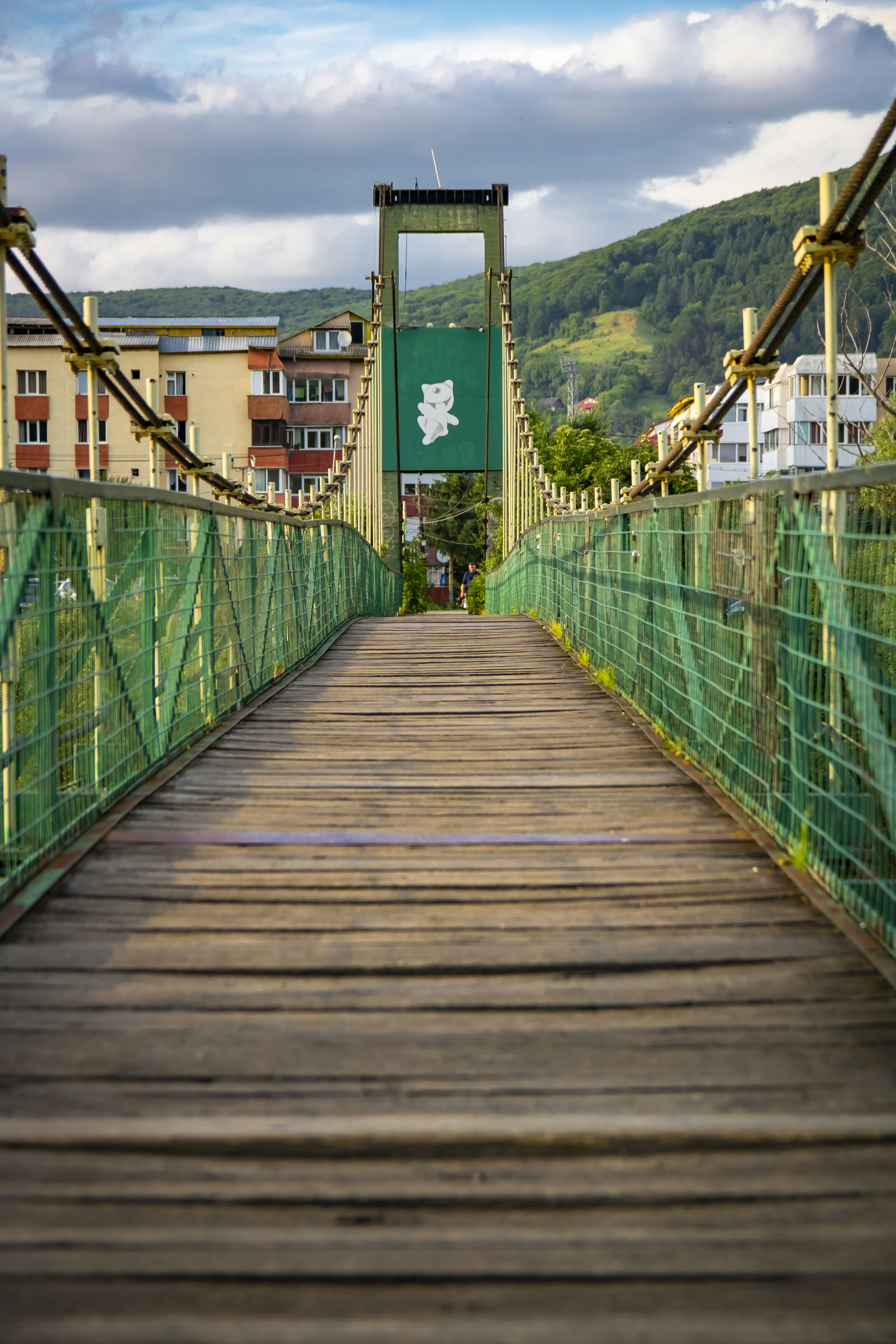 Emerald Span: A wooden pedestrian bridge guiding toward a hilltop town