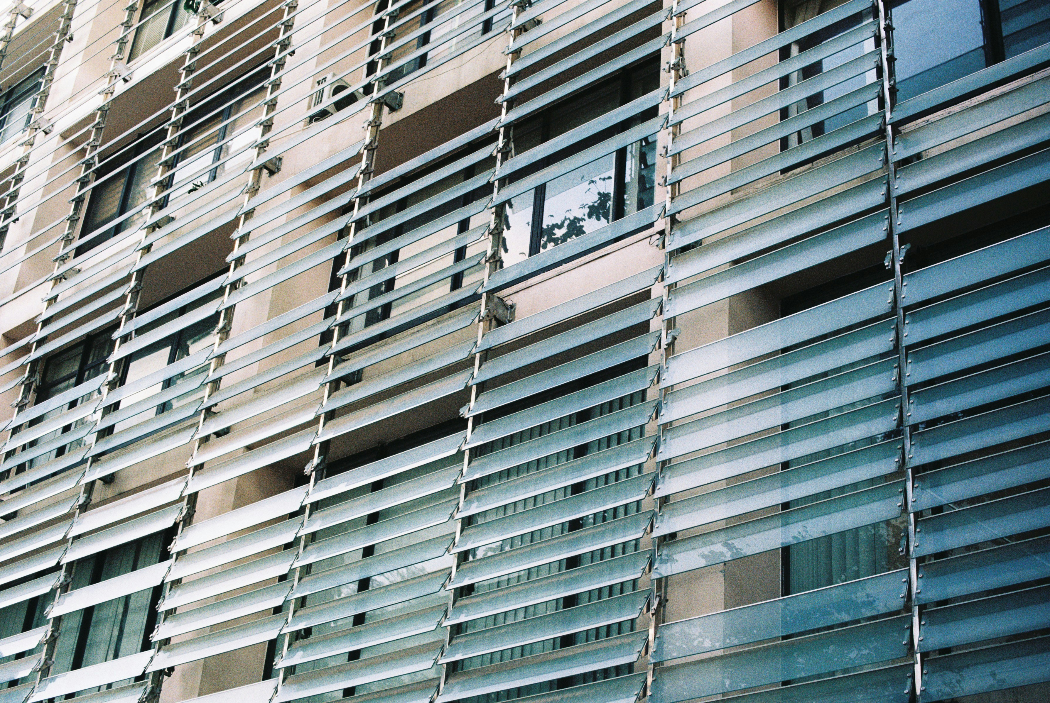 Modern building facade featuring horizontal metal slats and large glass windows, creating a dynamic interplay of reflections and shadows.
