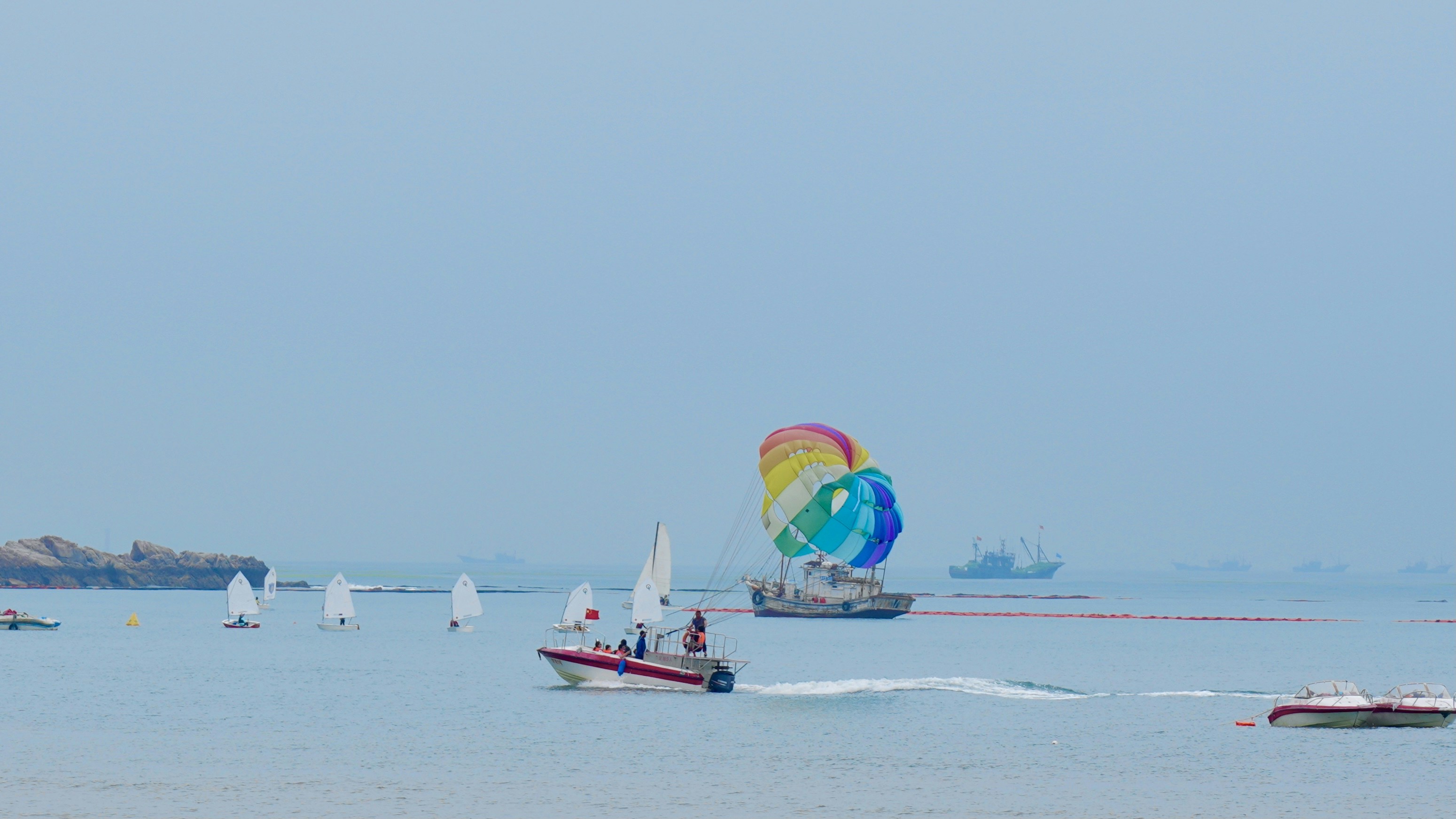 Vibrant sailboat with a rainbow-colored spinnaker gliding among smaller boats on a calm sea.