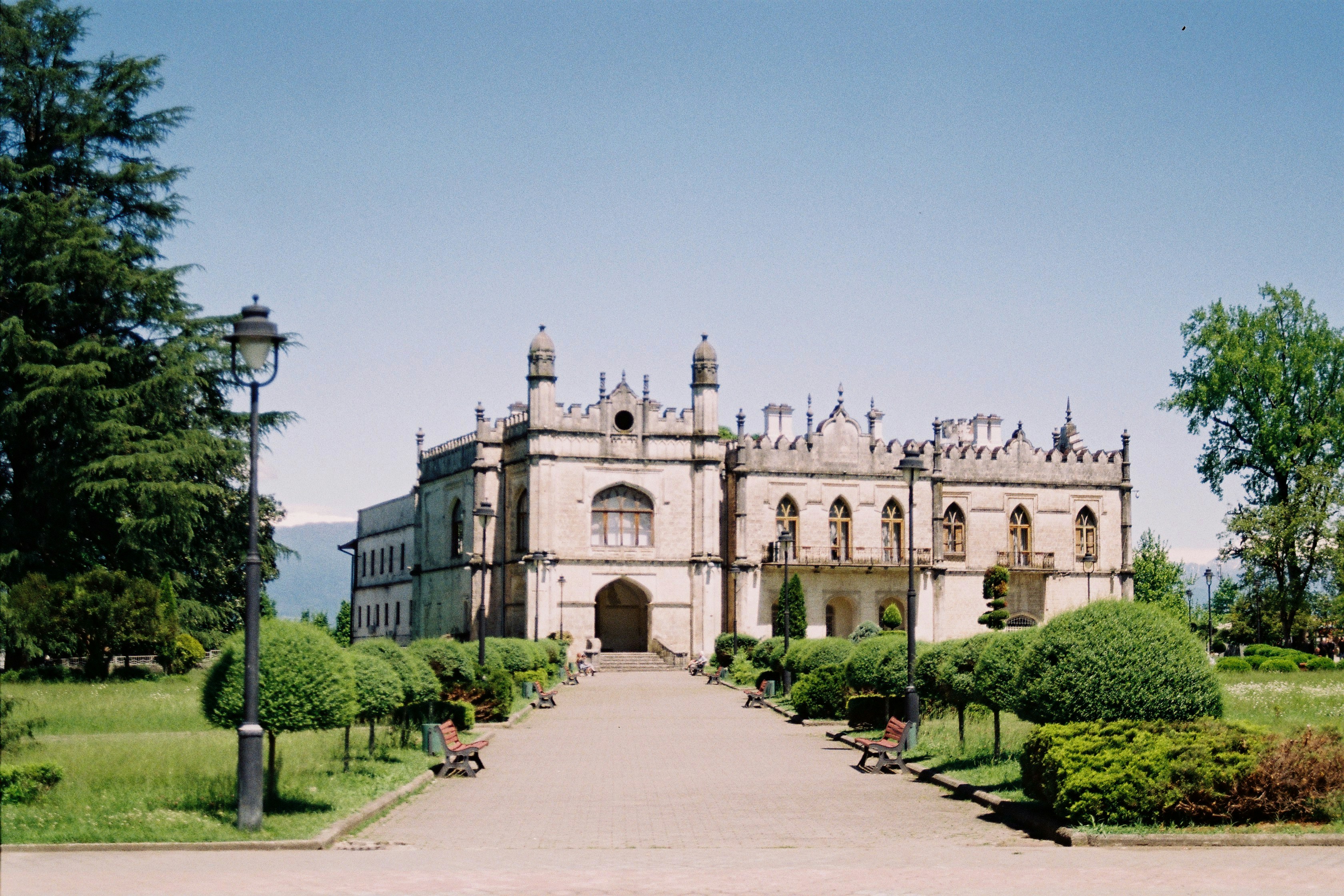 Historic mansion framed by manicured hedges and towering trees, showcasing intricate architectural details and a welcoming pathway.