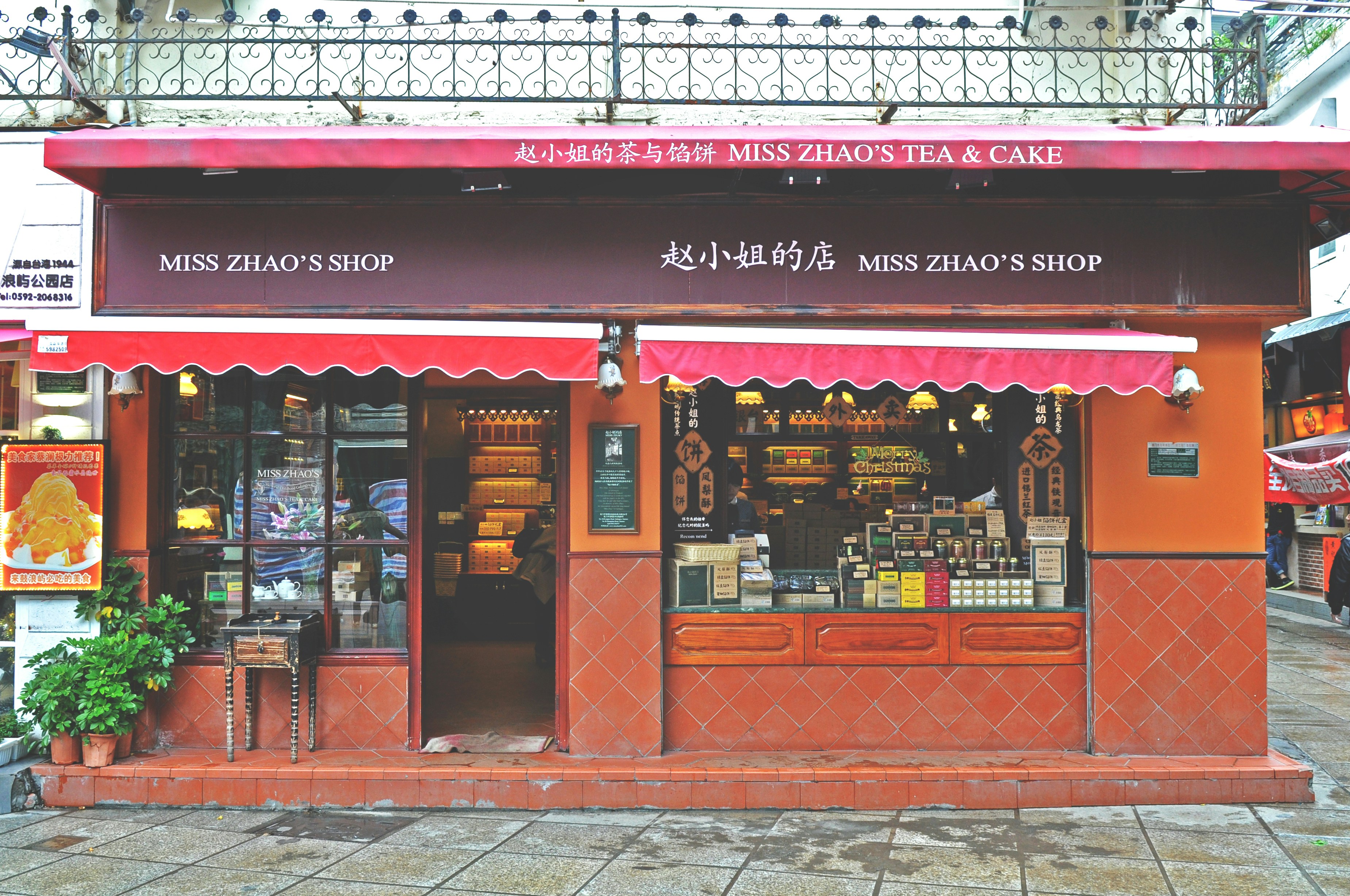 Charming storefront of Miss Zhao's Tea & Cake, featuring an inviting display of teas and pastries under a vibrant awning. The shop's warm colors and intricate signage add to its welcoming atmosphere.