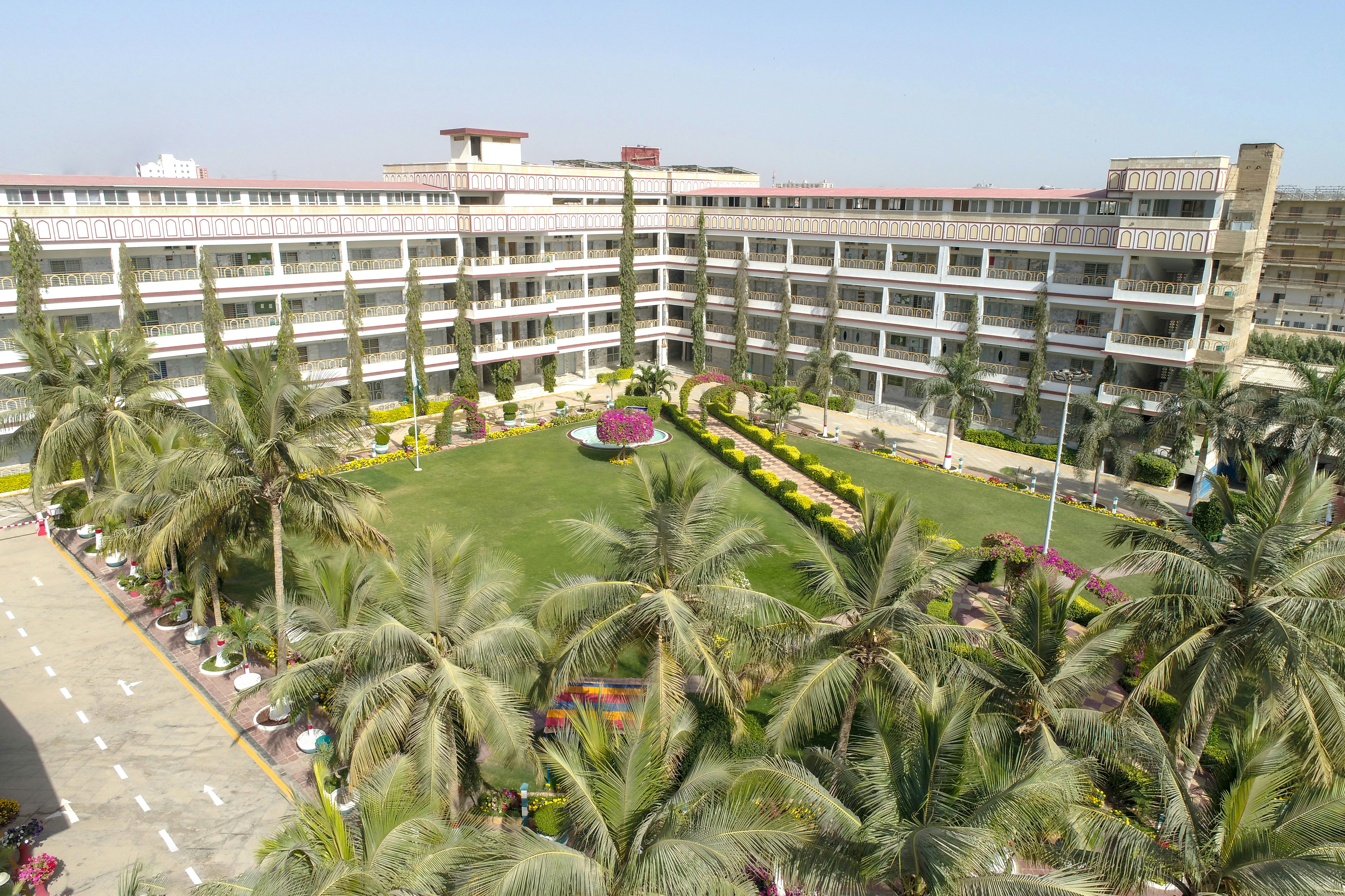 Aerial view of a large institutional building surrounded by lush greenery and palm trees under a clear blue sky.