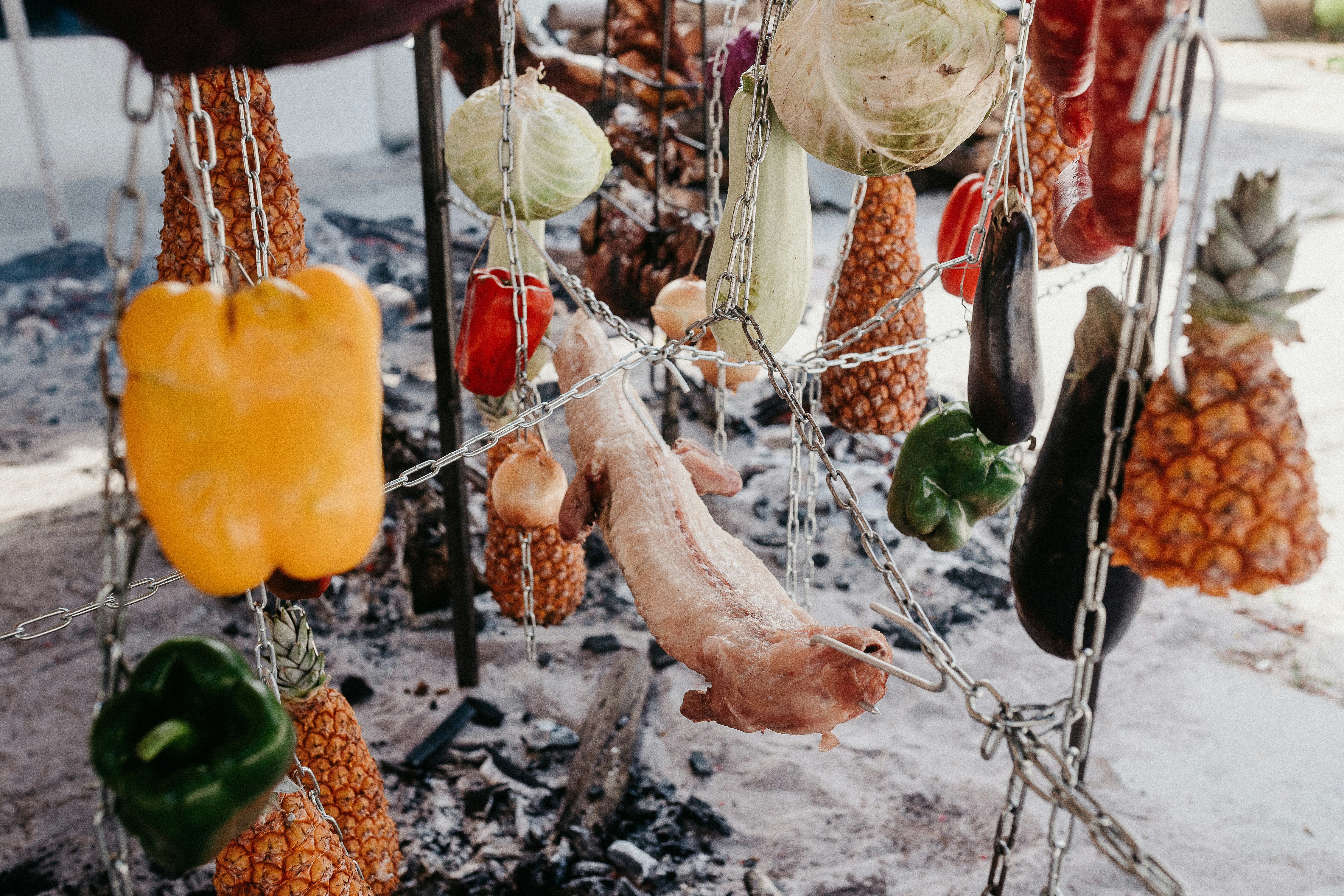 An array of colorful vegetables and a hanging piece of meat suspended from chains, showcasing a vibrant market scene.
