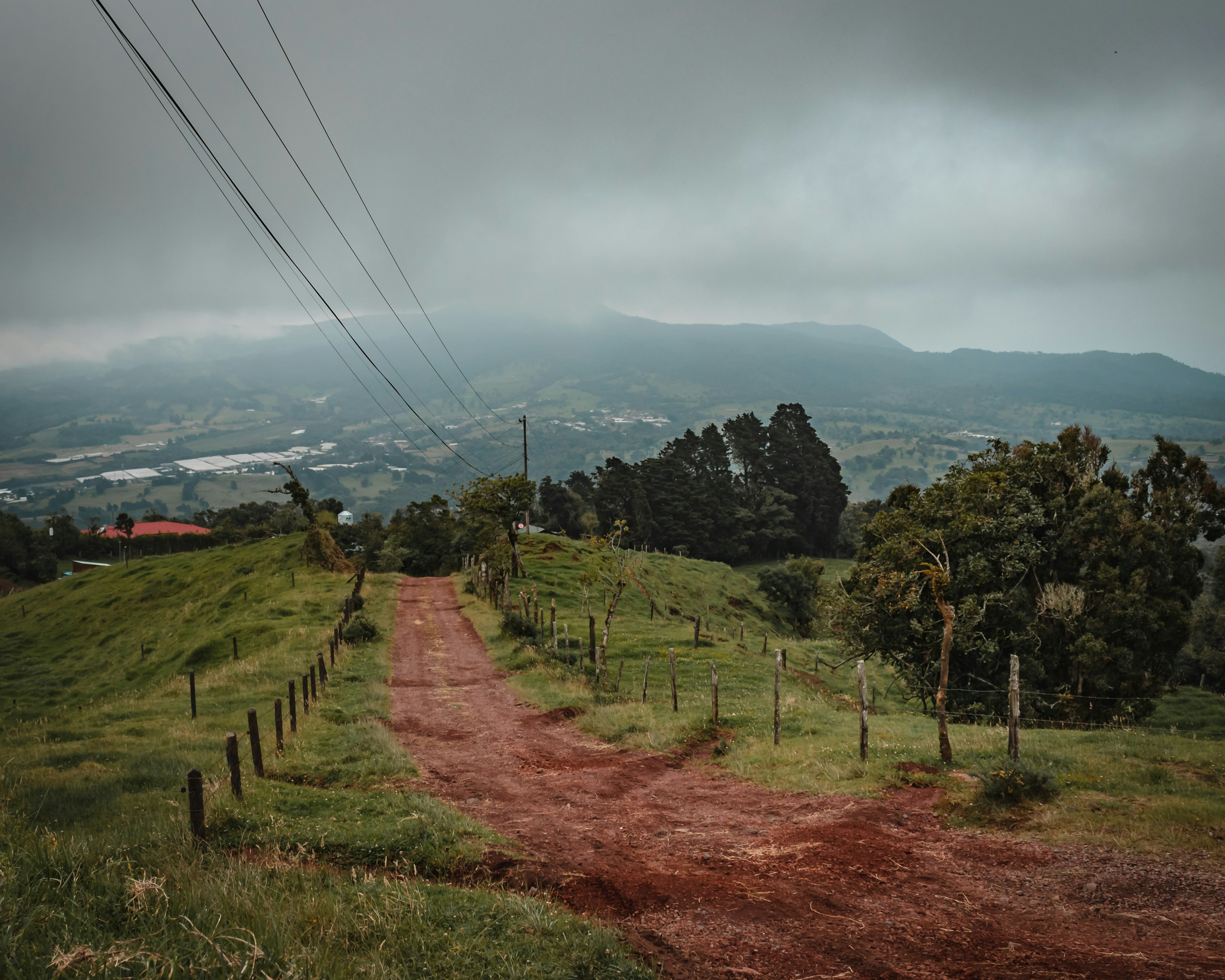 Rugged Dirt Road Winding Through Fence-Edged Hills Under Overcast Skies